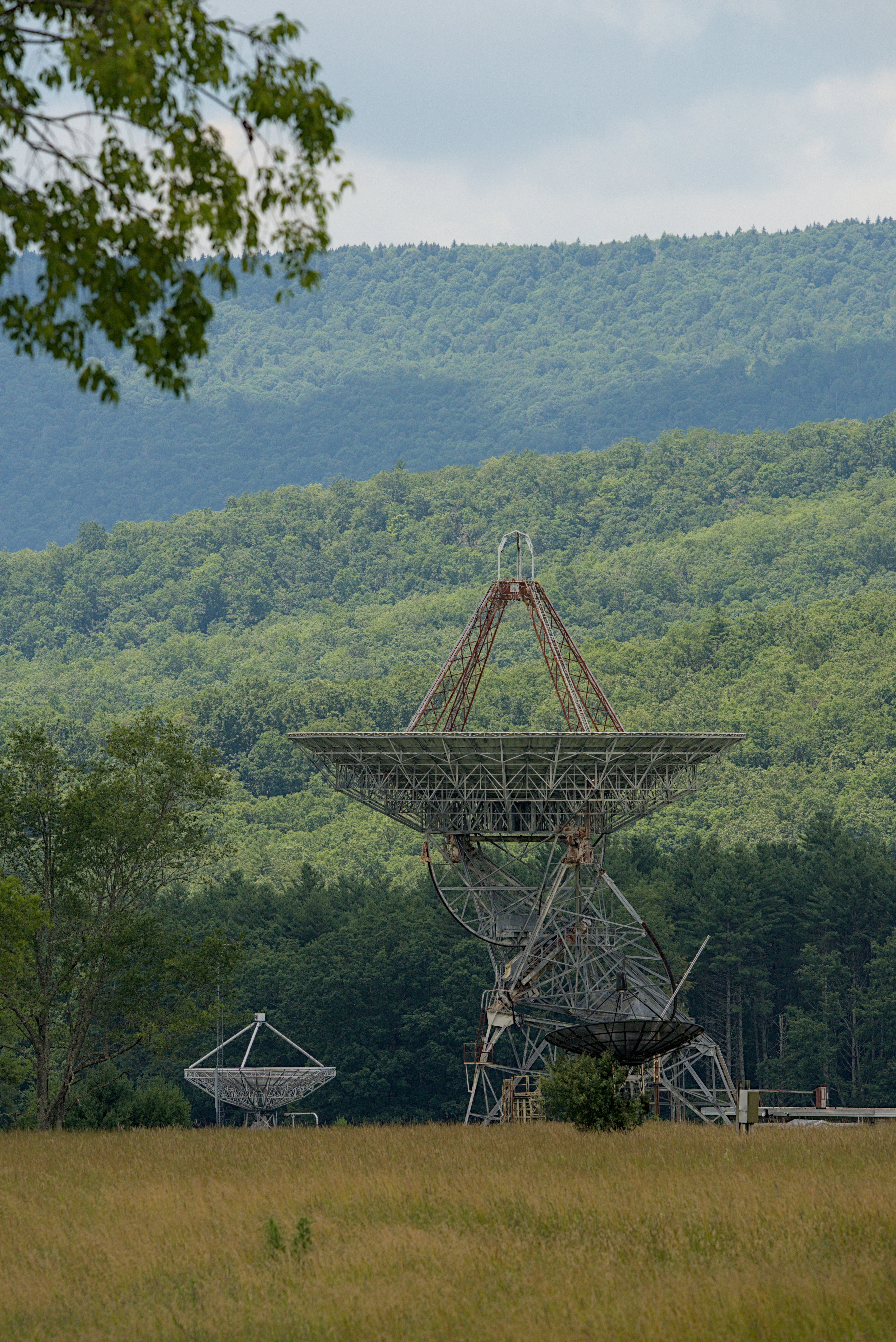 Two large satellite dishes stand amidst a lush green landscape, surrounded by rolling hills and a gentle sky, symbolizing the intersection of technology and nature.