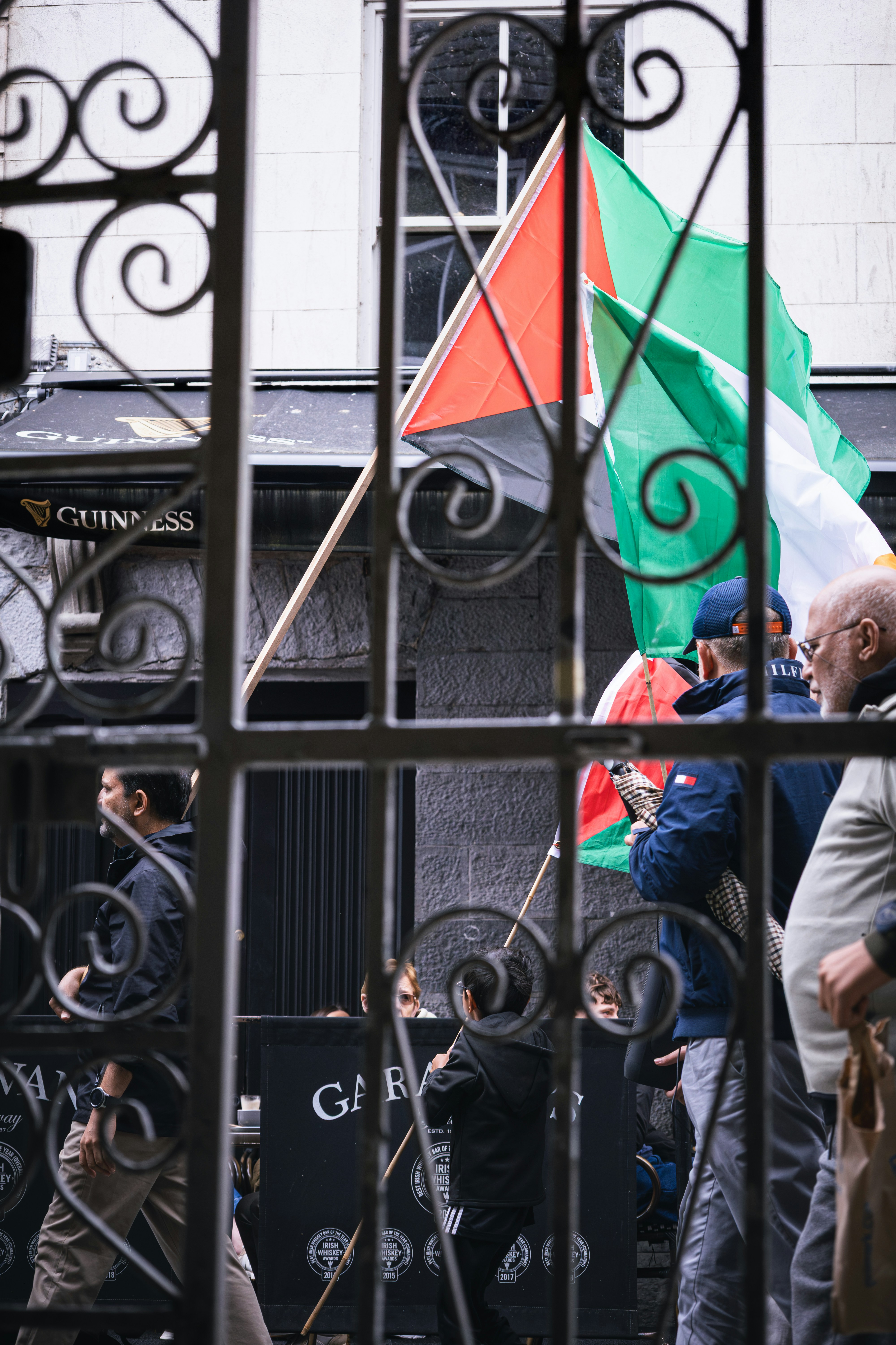 Flag Rising Behind Wrought-Iron Grilles on a Bustling Street