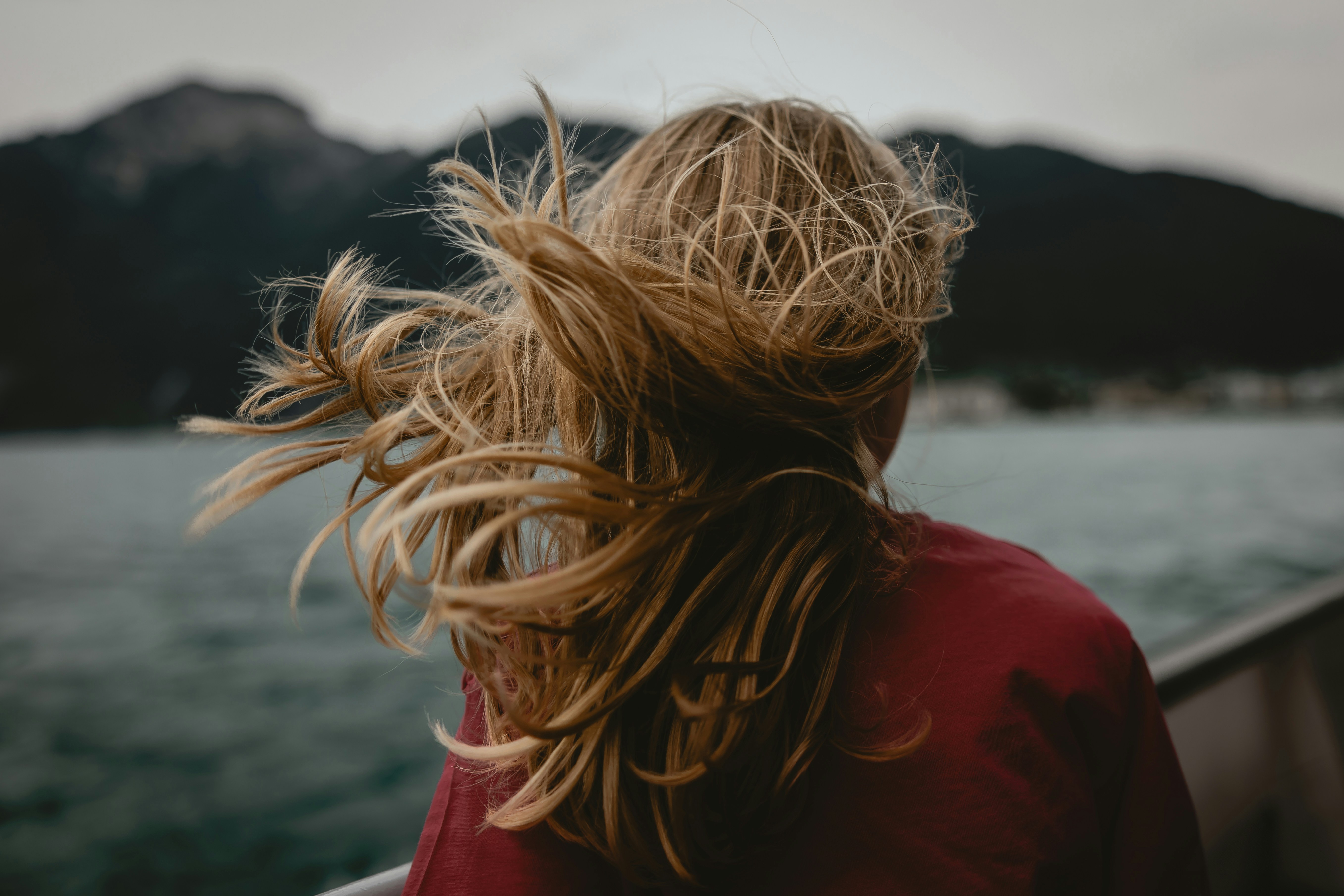 A woman with flowing hair gazes at the vast waters, embodying a moment of freedom and exploration. The backdrop features mountains shrouded in mist.