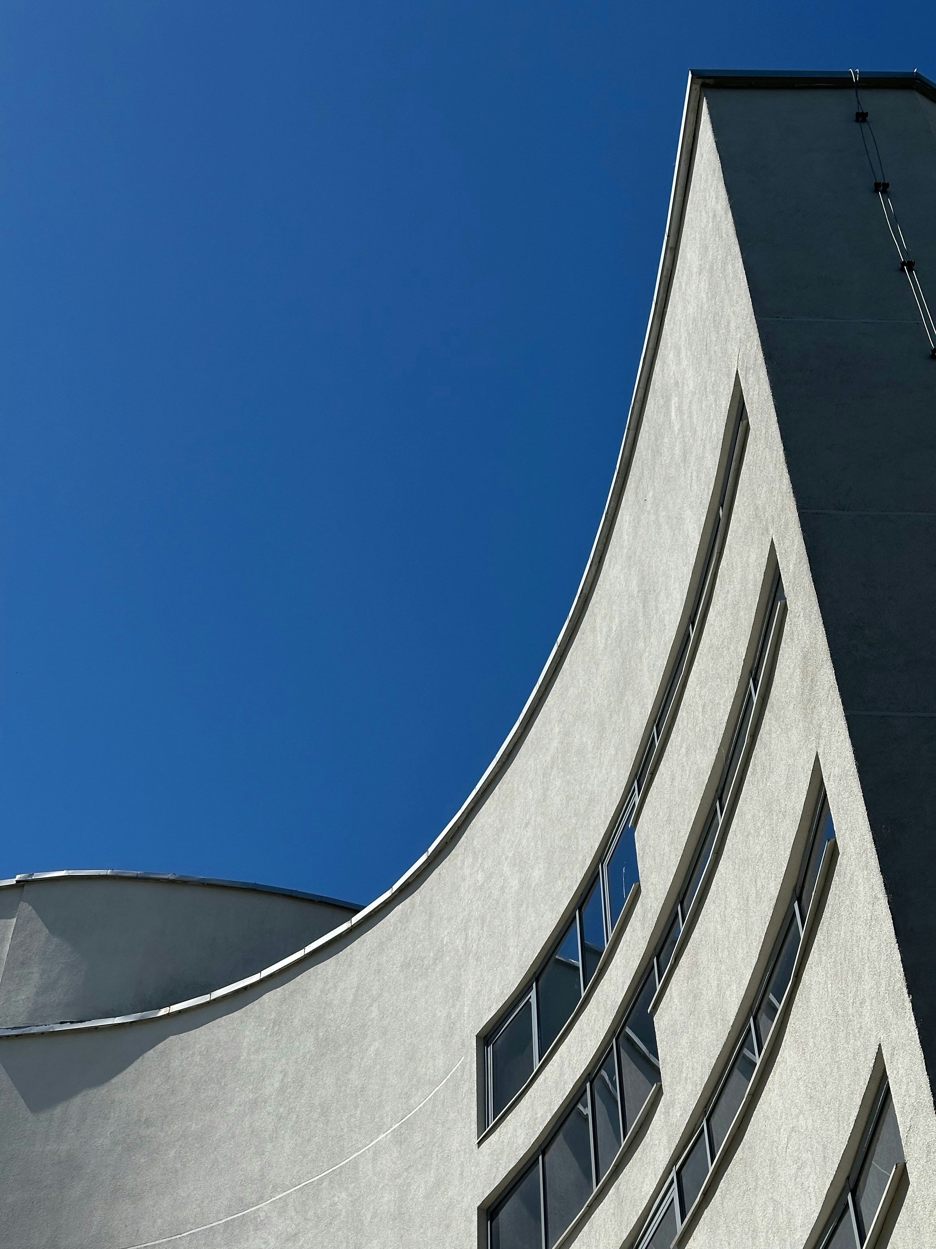 Modern building with a sweeping curved facade and large windows set against a clear blue sky.