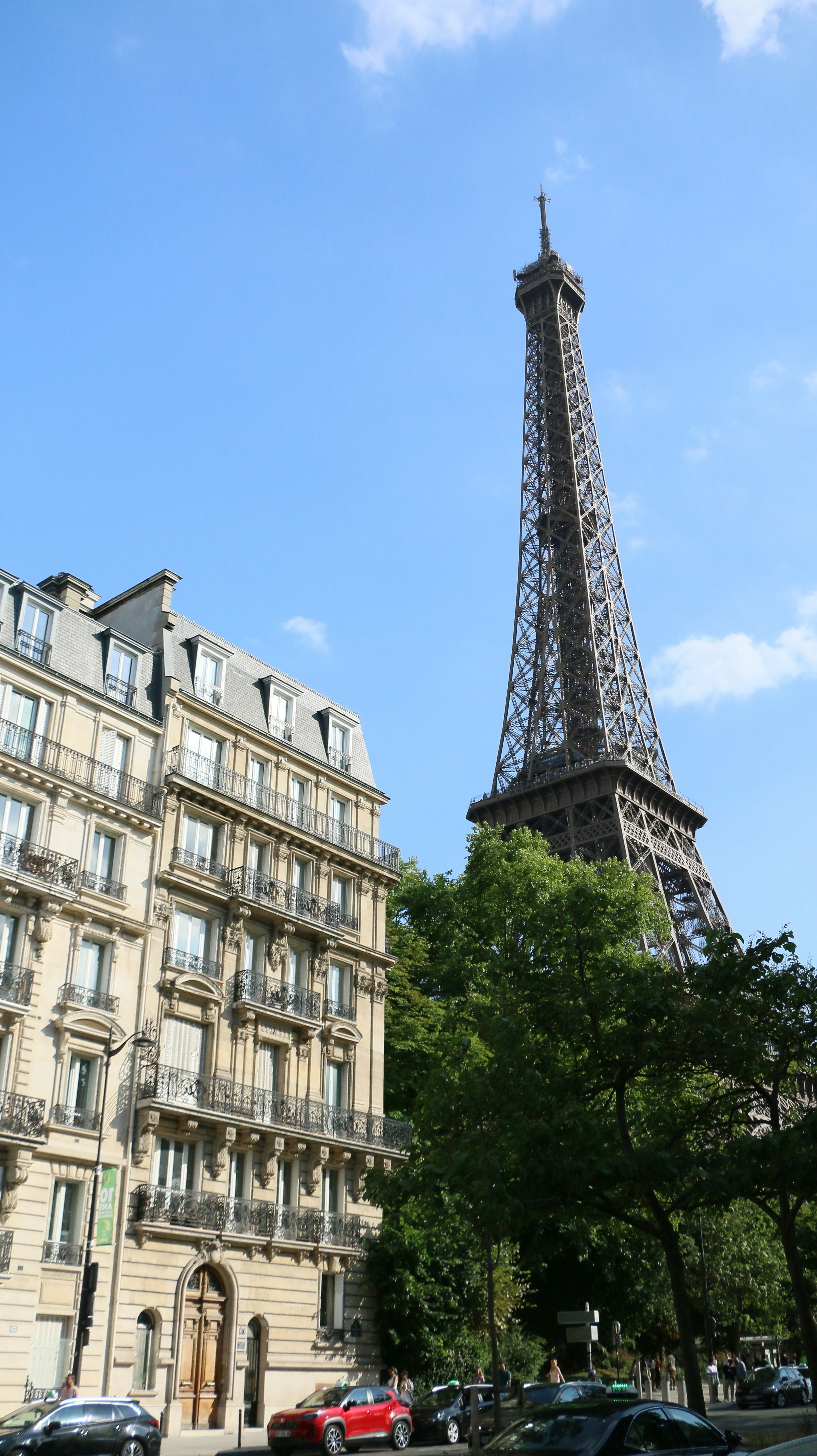 Eiffel Tower rising above classic Parisian architecture, framed by lush greenery and a clear blue sky.