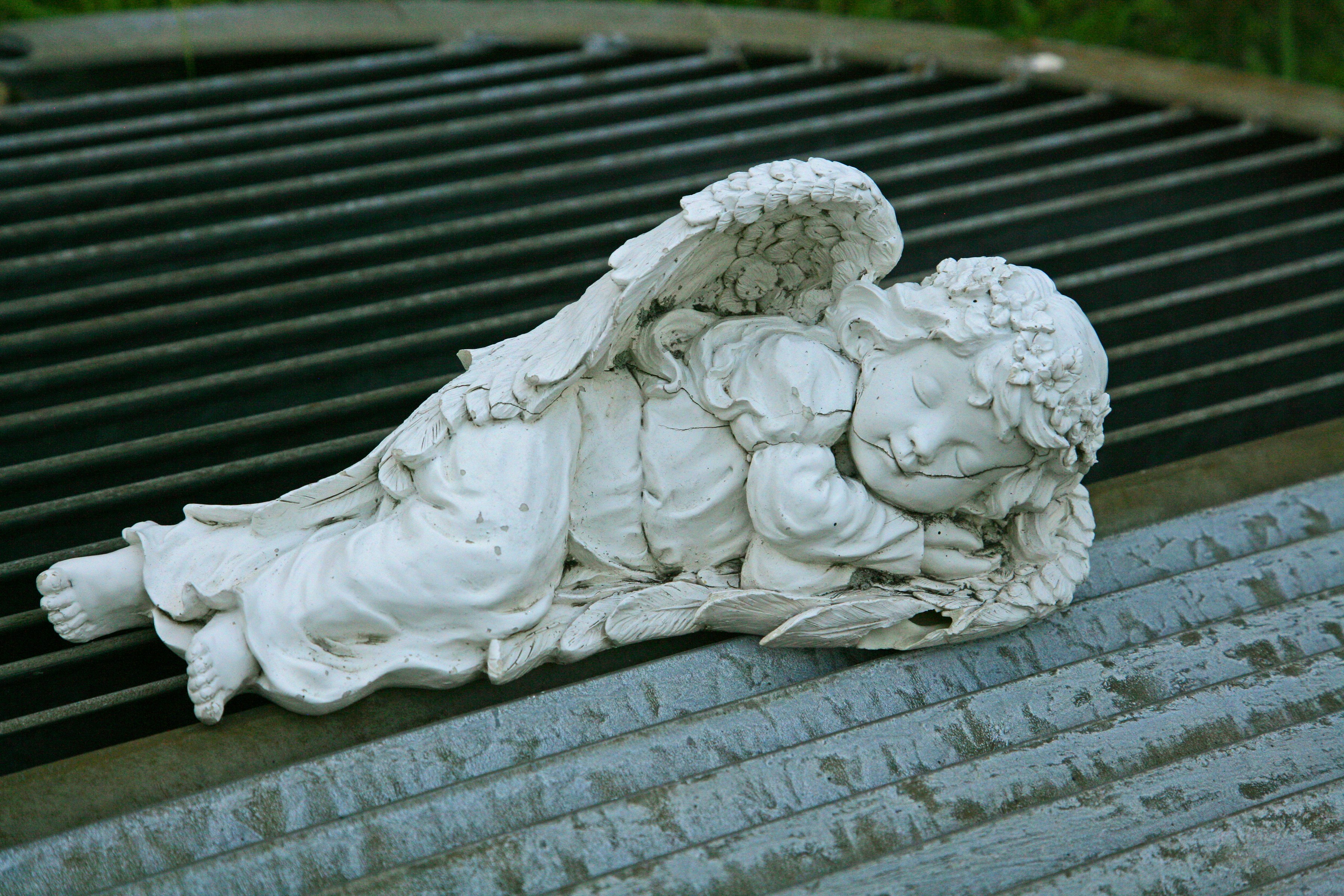 A delicate white angel sculpture peacefully resting on a weathered surface, exuding tranquility and grace.