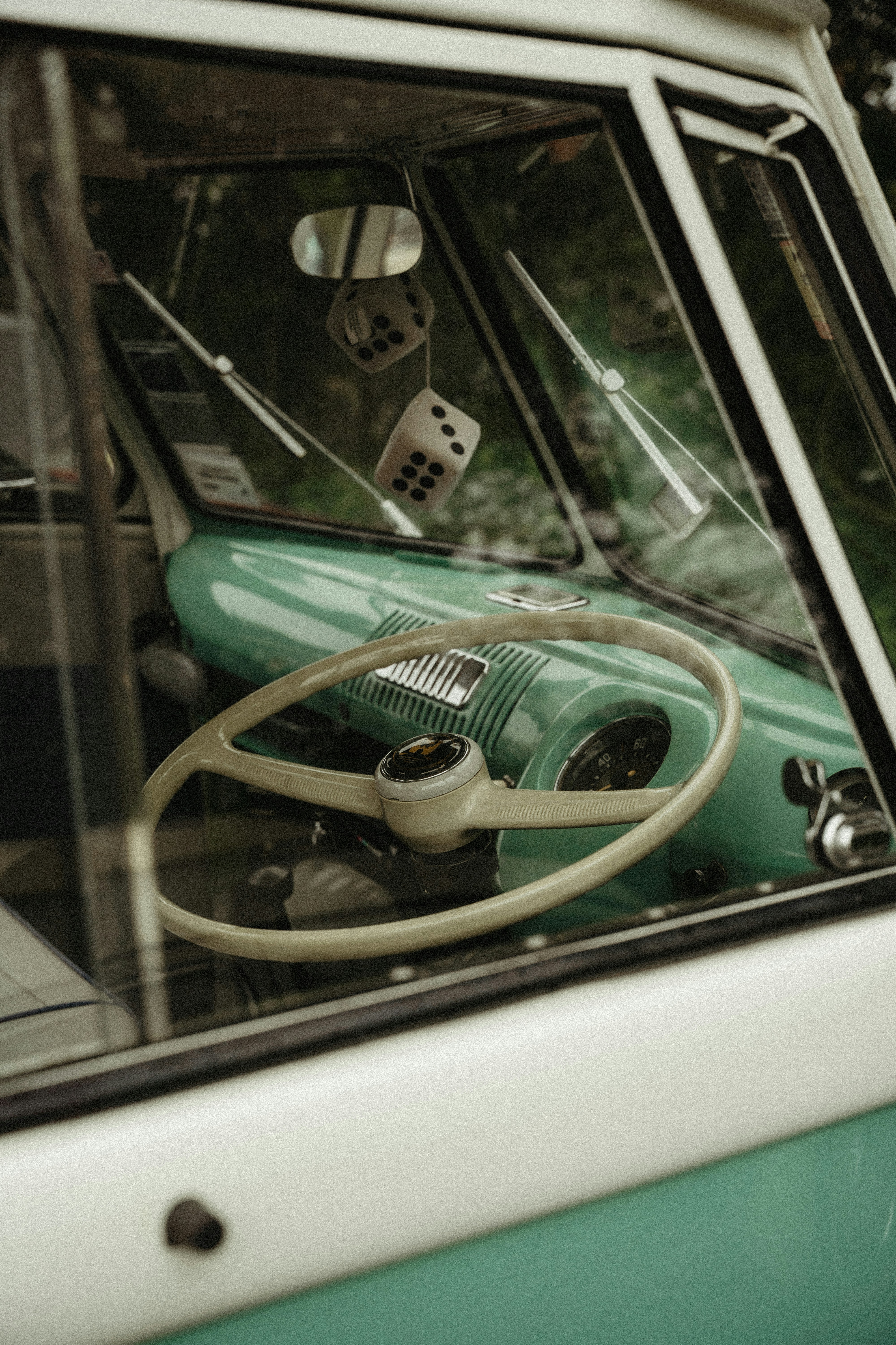 Interior close-up of a classic mint green Volkswagen Kombi, highlighting the wheel and dashboard in natural light. | Vintage car interior with dice hanging.