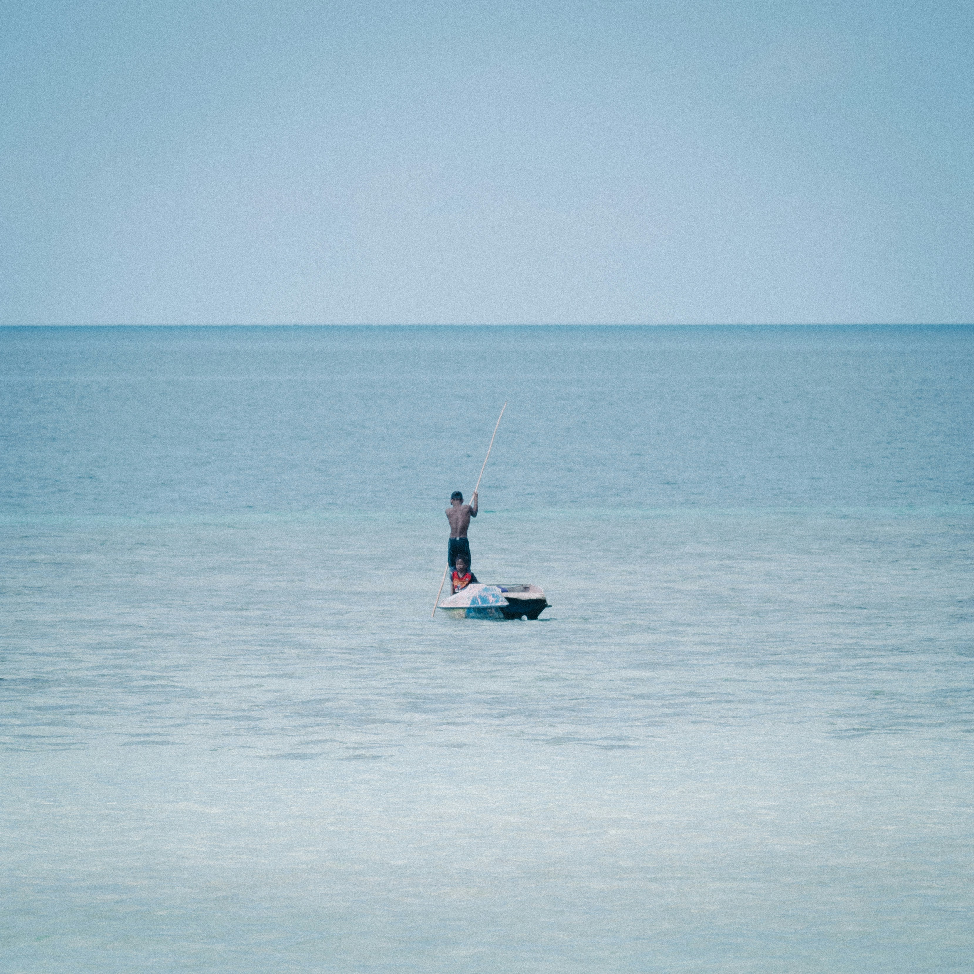 Man fishes while standing on a small boat.