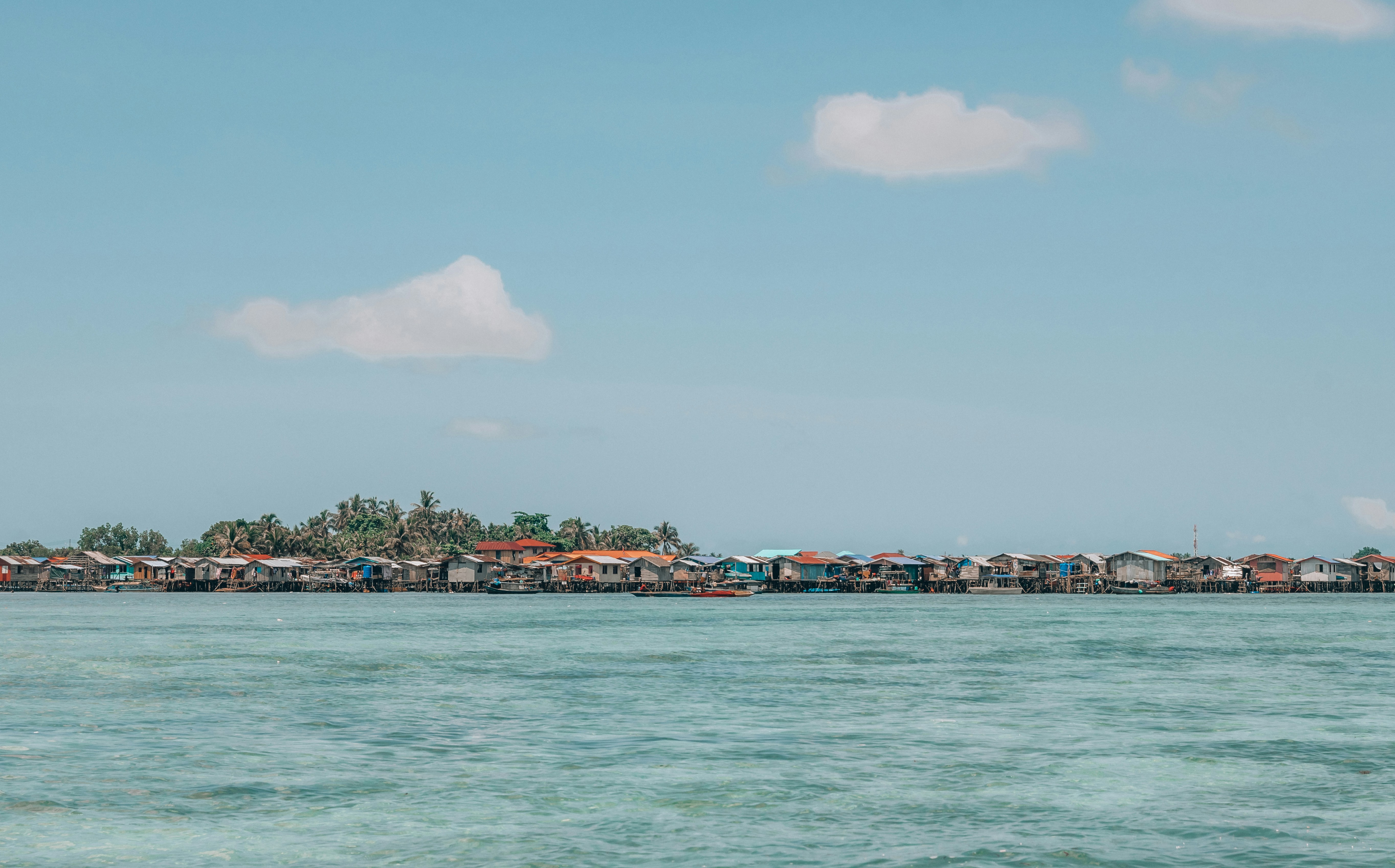 Colorful stilt houses line the coast against a backdrop of clear blue skies and tranquil waters. This scene captures the essence of life in a coastal village.