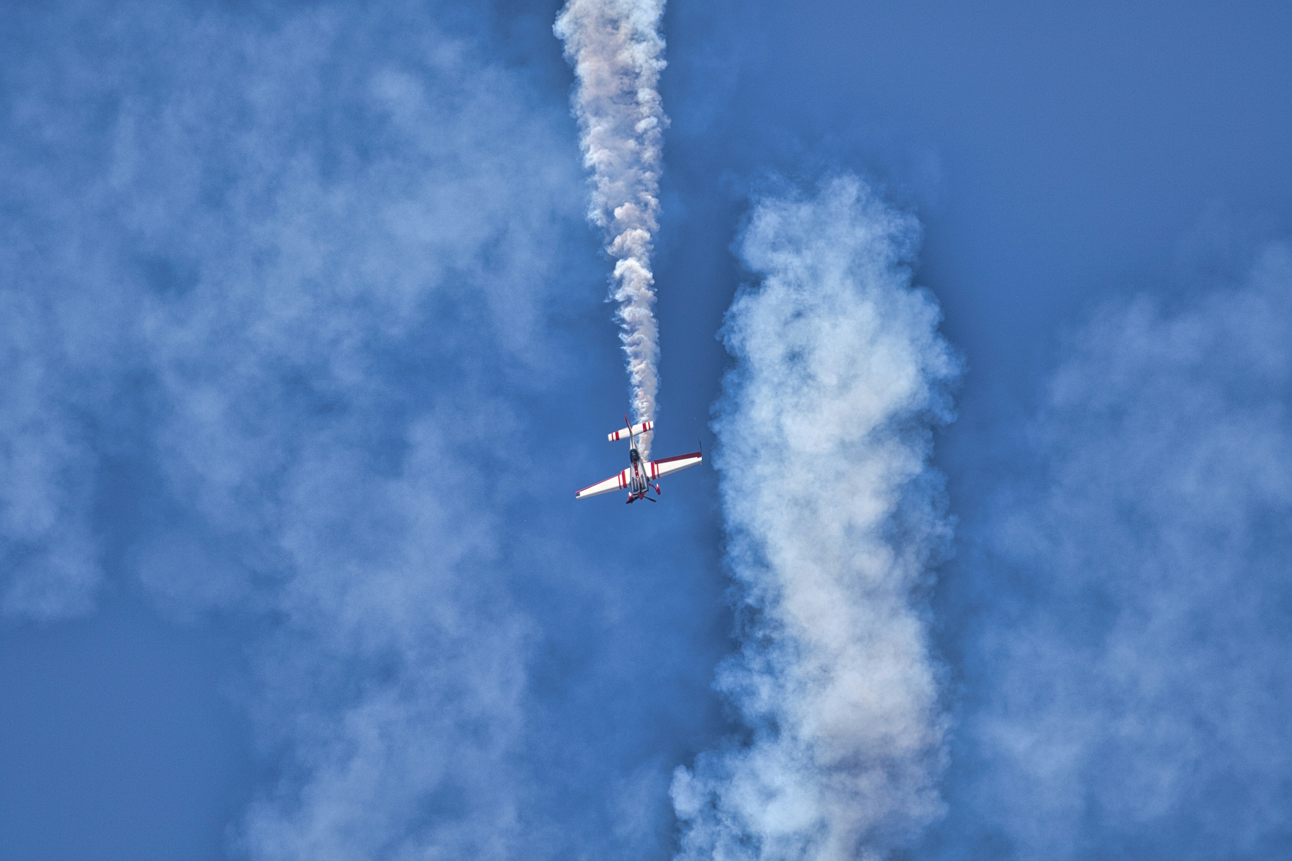 Aircraft performing a daring maneuver, leaving trails of smoke against a clear blue sky.