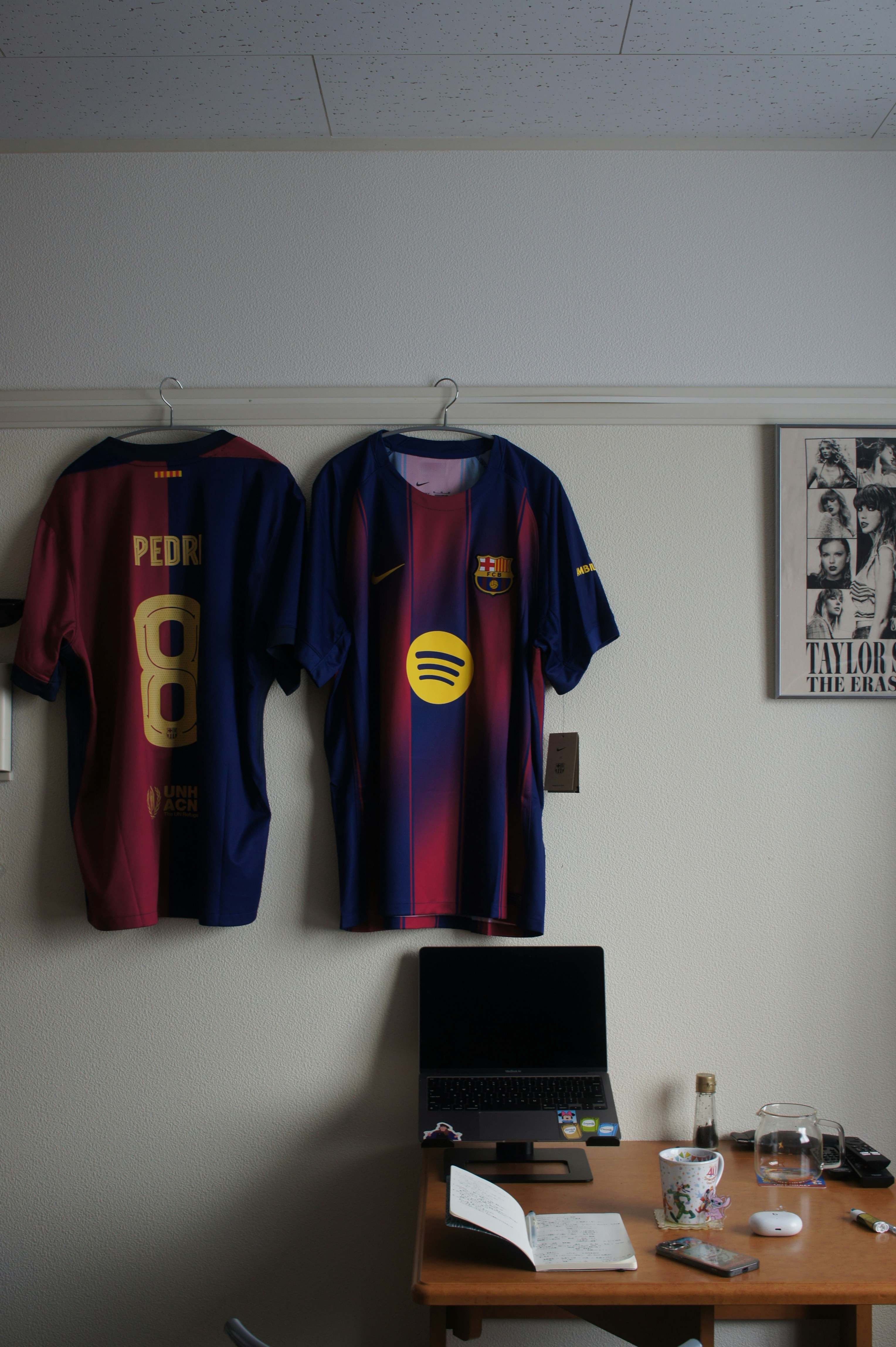 FC Barcelona's home kit | Soccer jerseys hang on a wall above a messy desk.