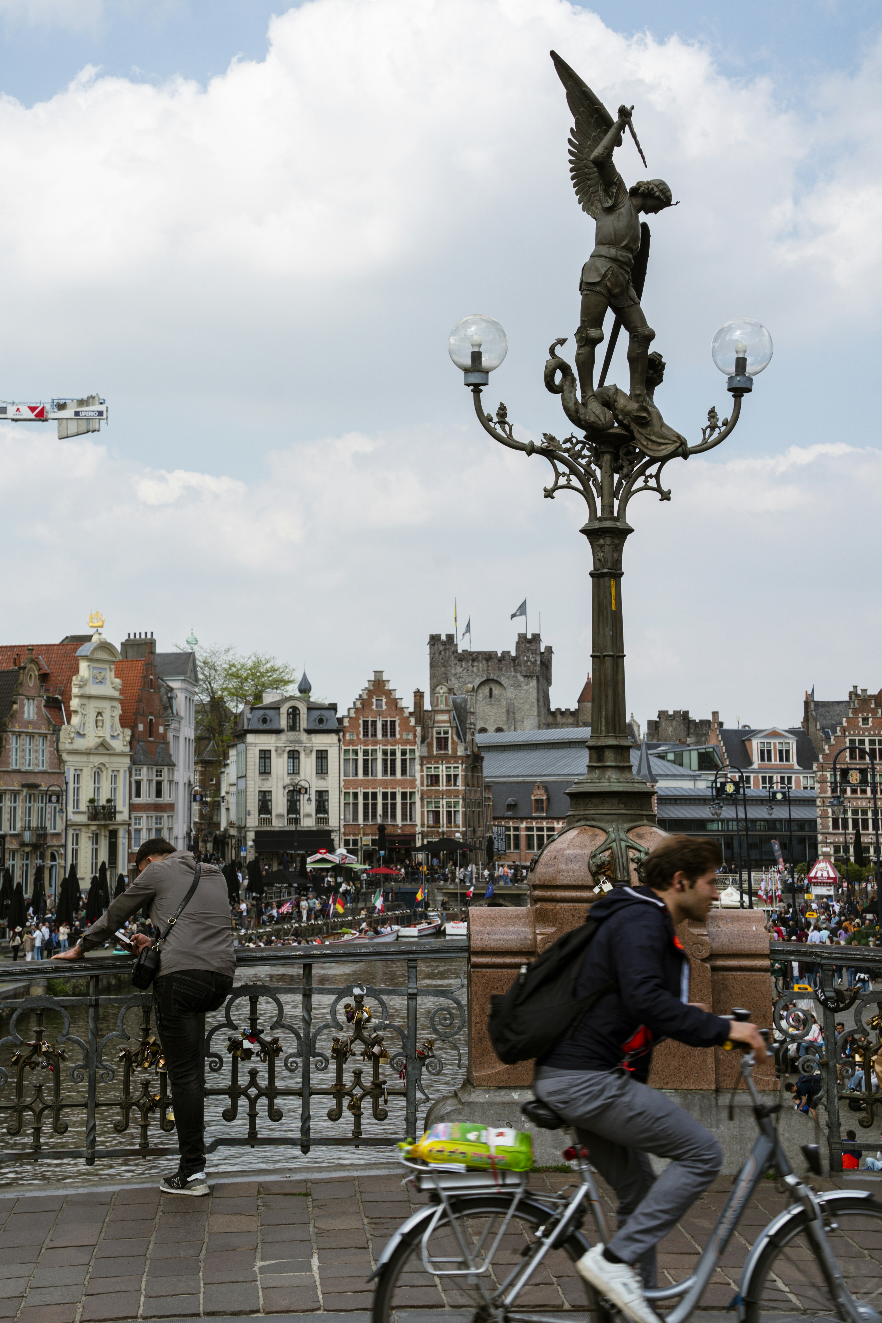 Angel over the Market: A Winged Statue Casting Long Shadows on a Busy Belgian Canal