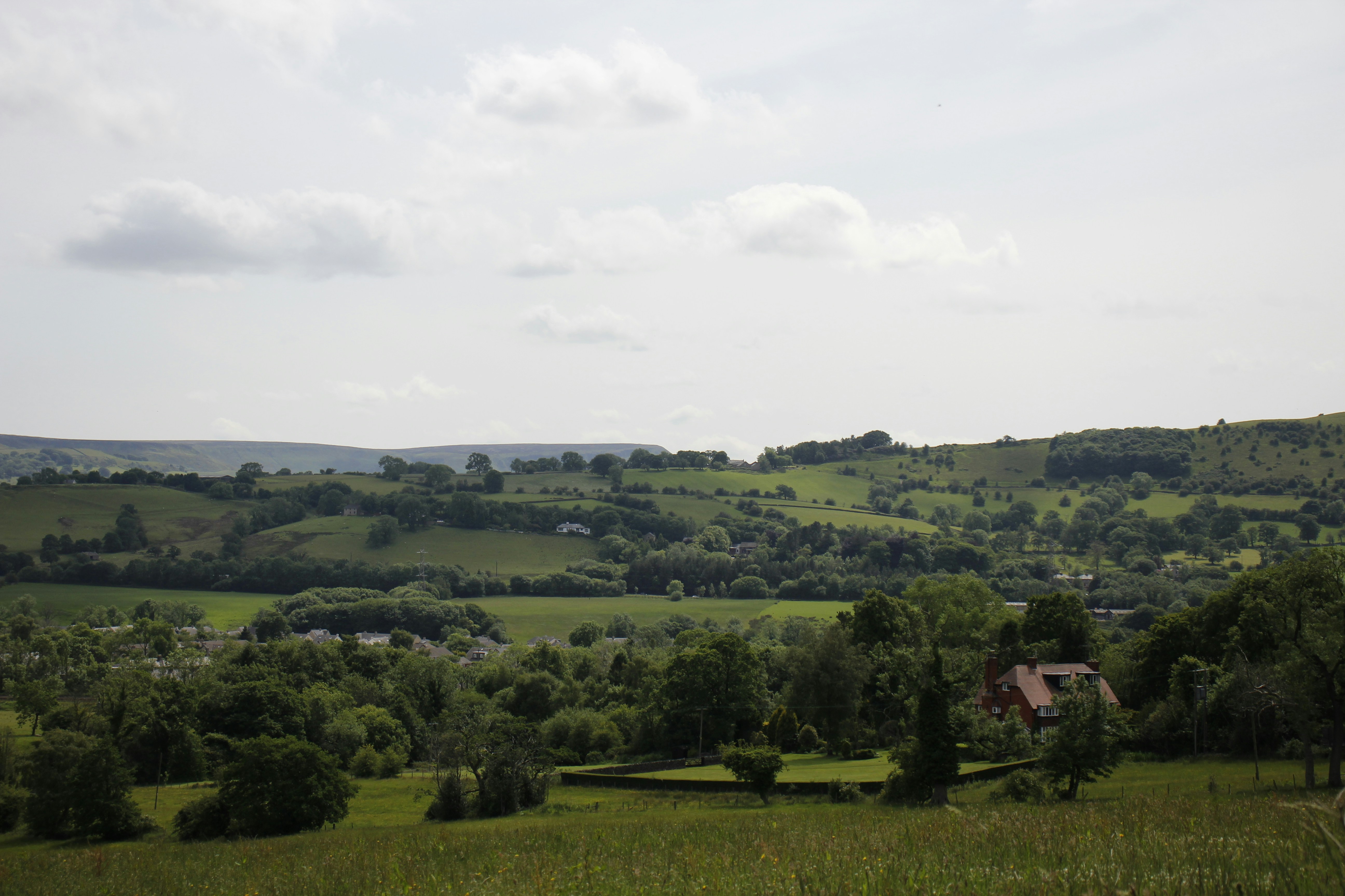 Lush green hills stretch across the landscape, dotted with trees and a quaint house nestled in the foreground. Soft clouds drift above, enhancing the tranquil atmosphere.