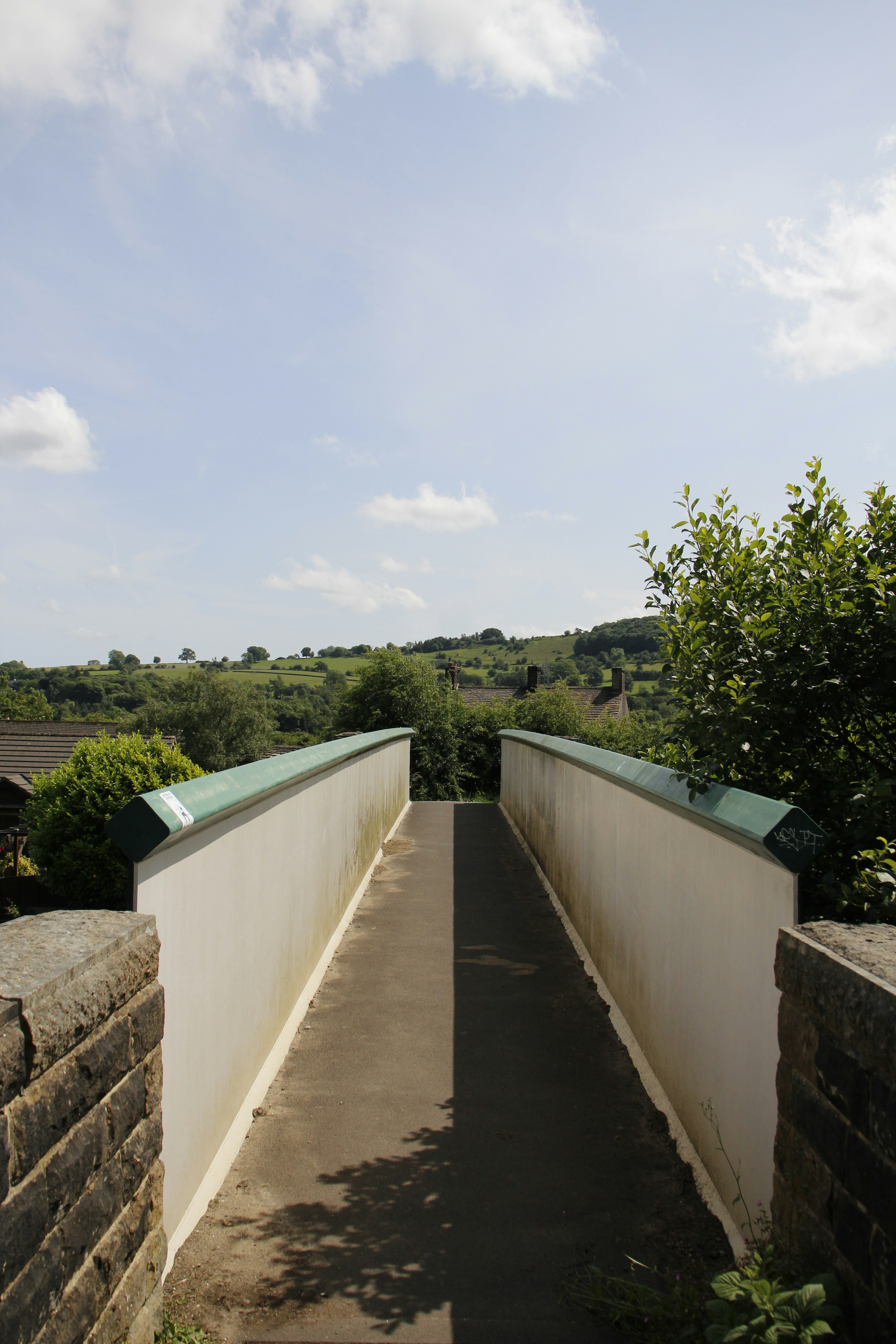 A bridge leads to greenery under a blue sky.