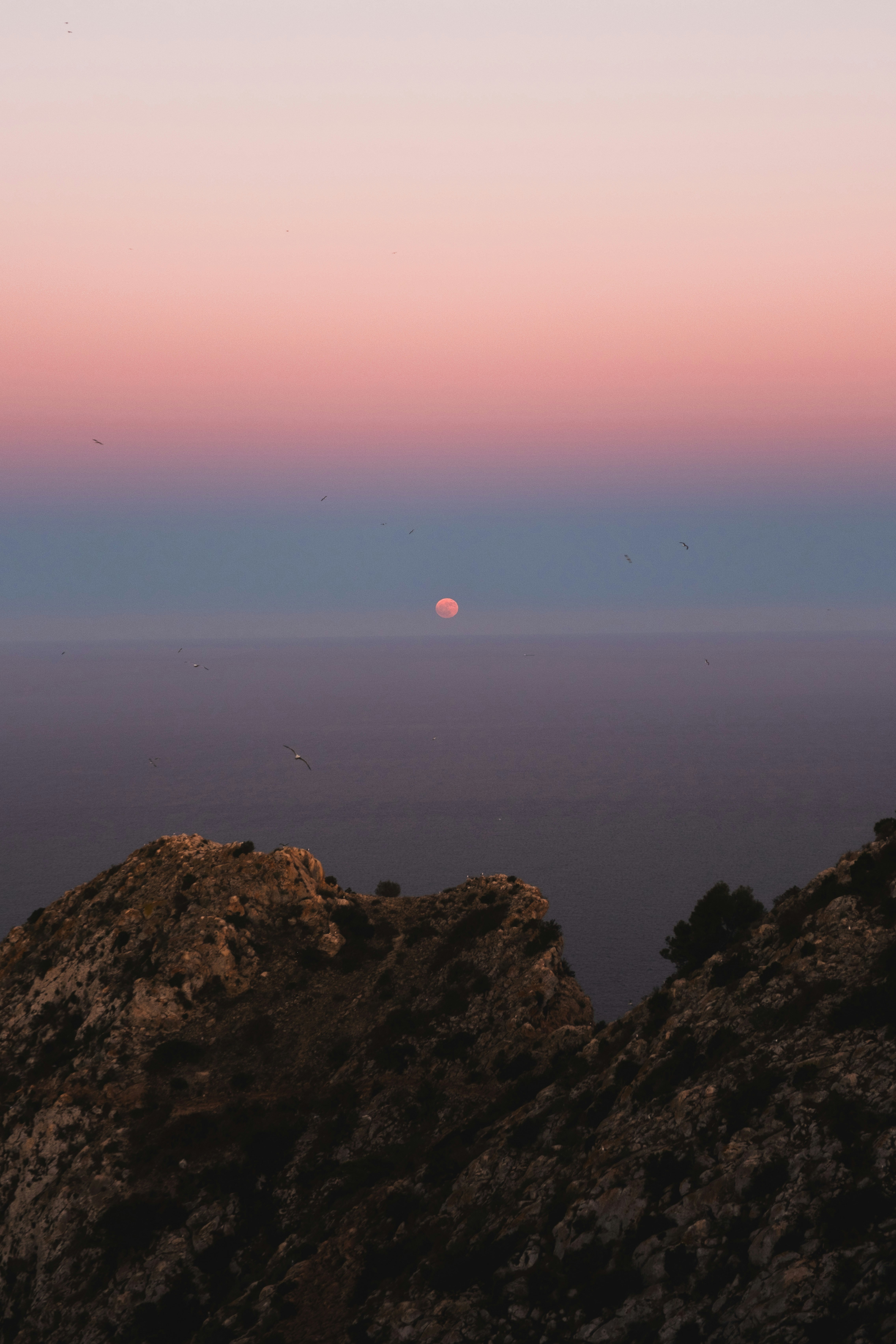 The moon rises over a misty, colorful horizon.