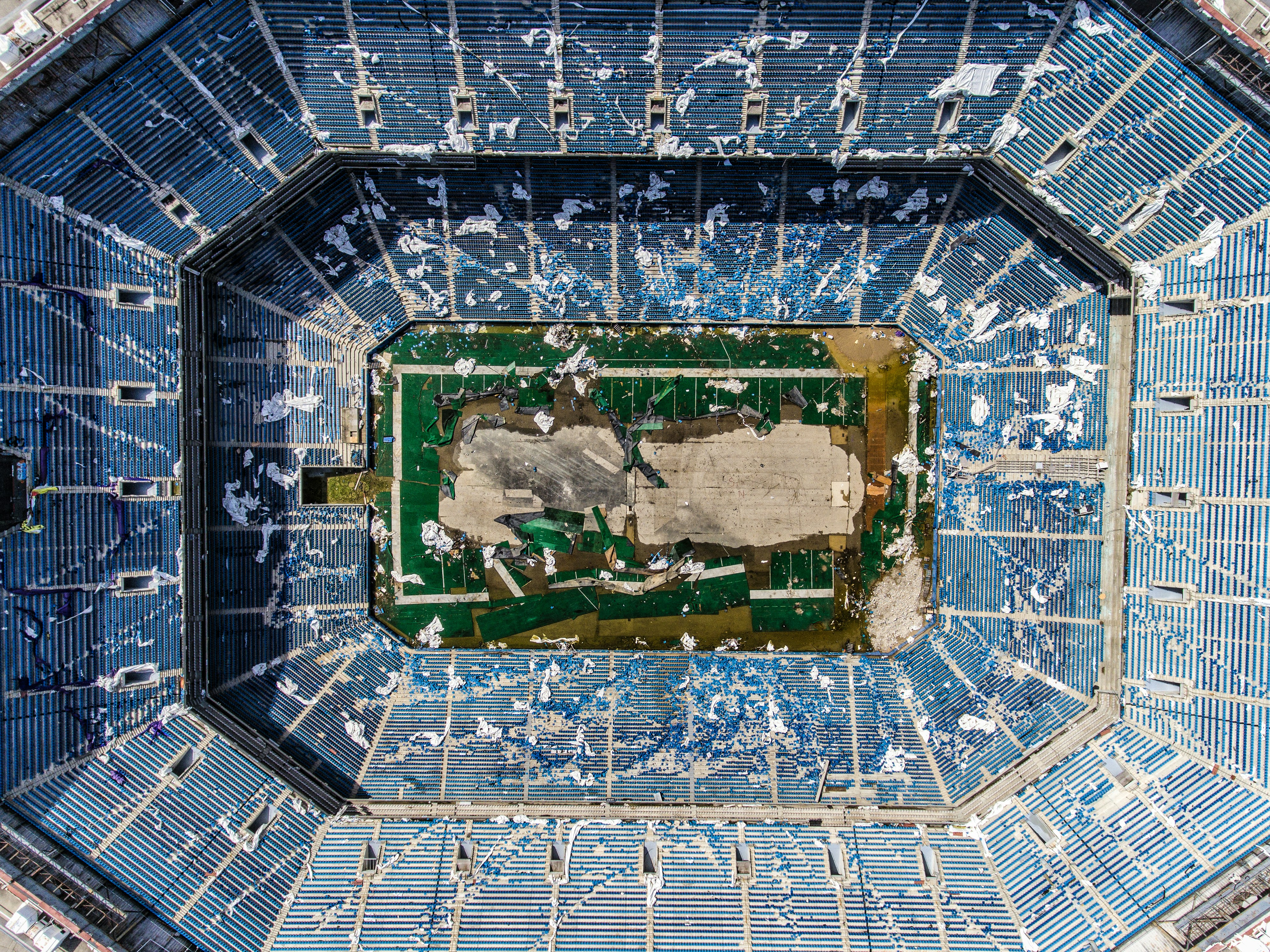 Aerial view of an abandoned stadium with scattered debris and a worn-out field, showcasing the passage of time and neglect.