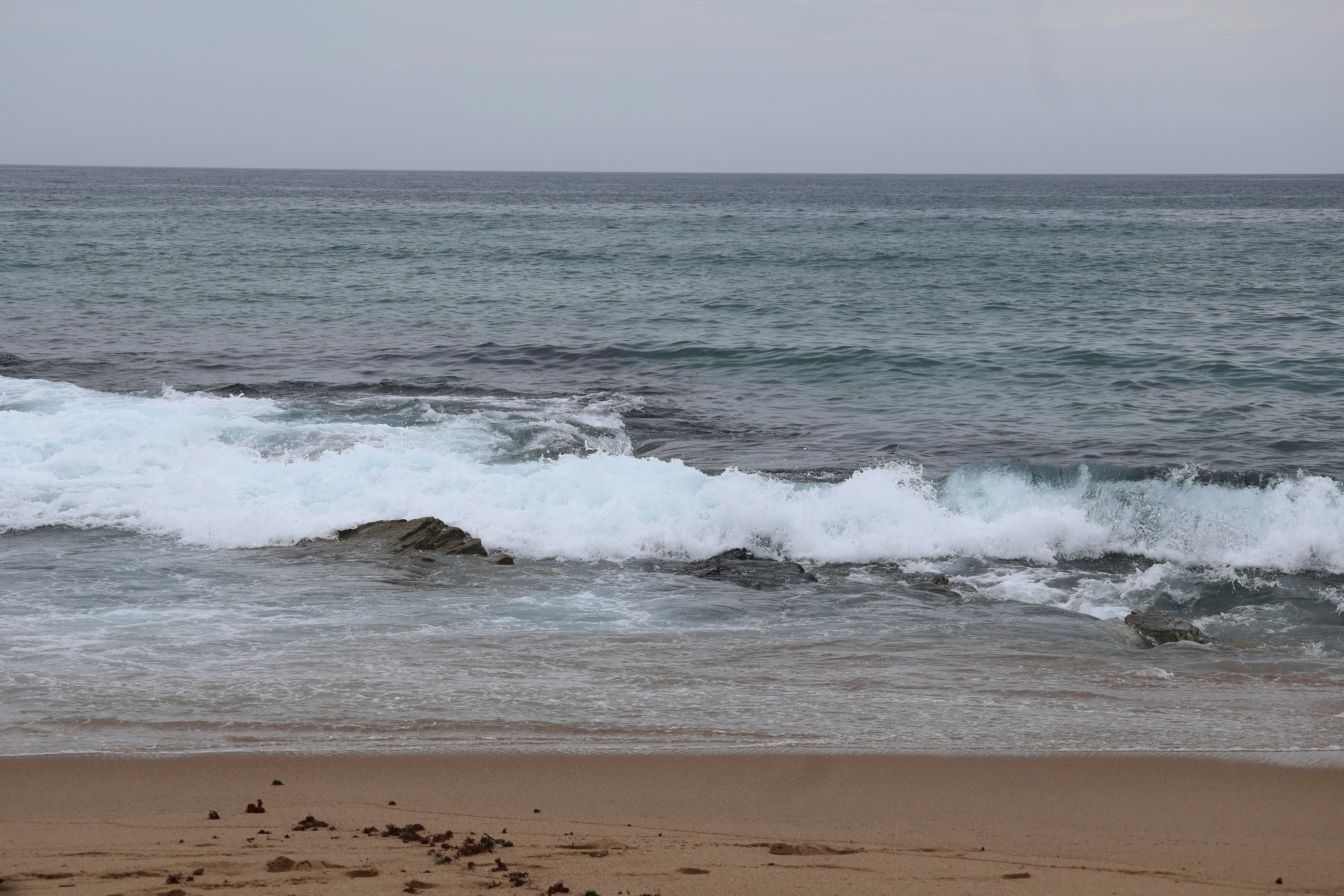 Waves crash on the shore during a cloudy day.