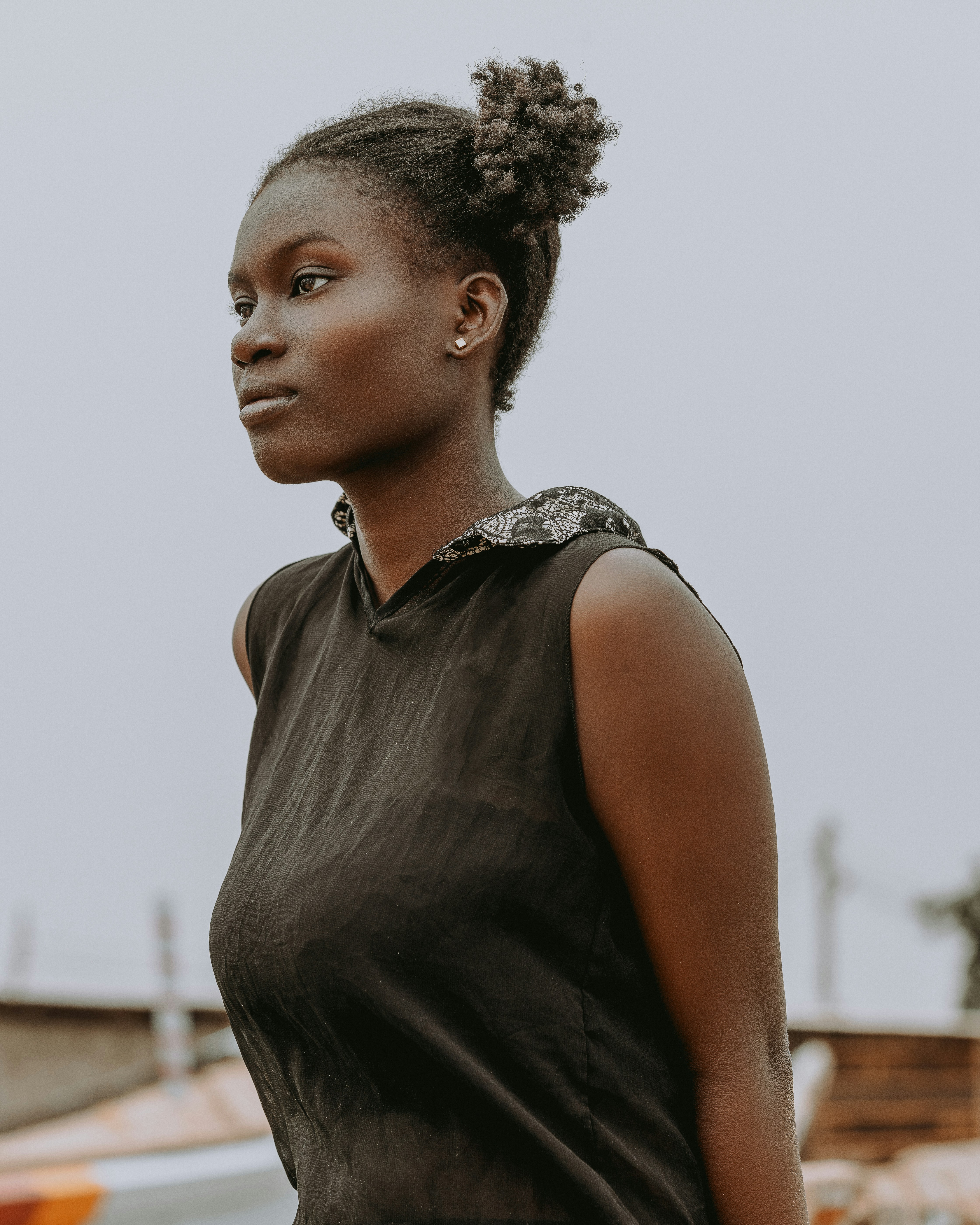 Young woman in a black sleeveless top stands thoughtfully against an urban backdrop, embodying resilience and introspection.