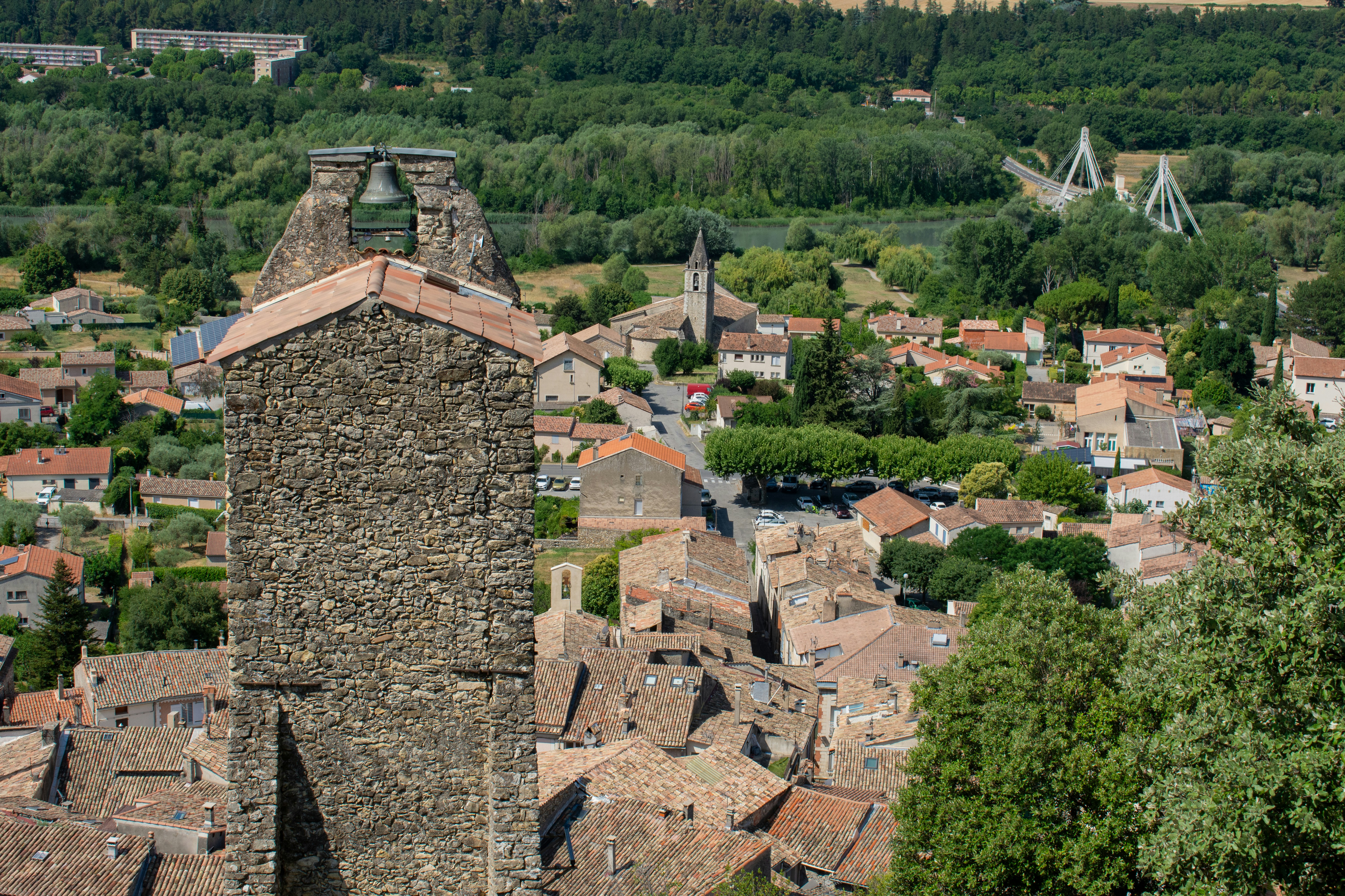 Historic stone tower rises above a quaint village, surrounded by lush greenery and modern bridges in the distance.