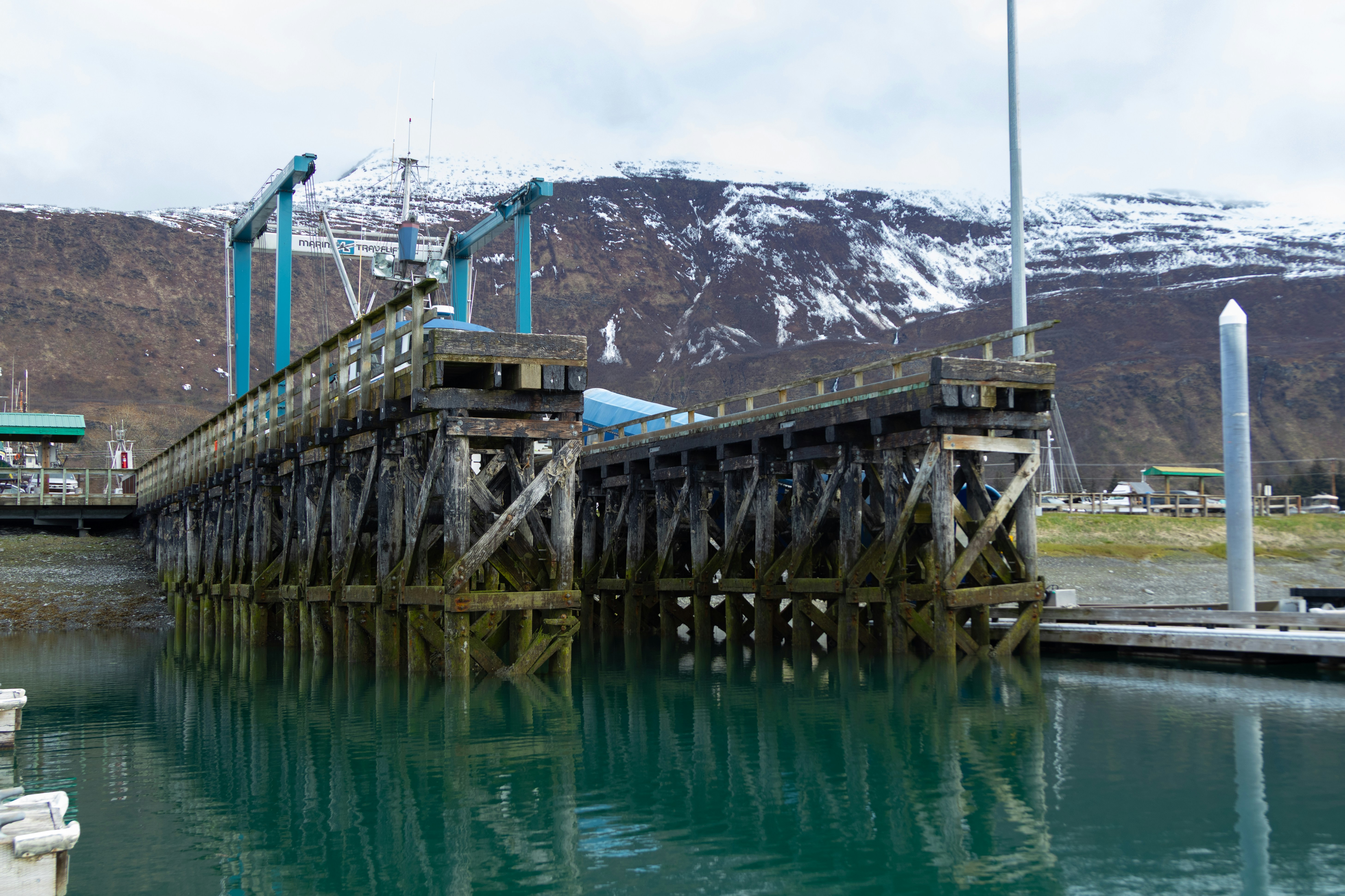 Aged Timber Pier Reaches Over Teal Fjord Toward Snow-Lined Peaks