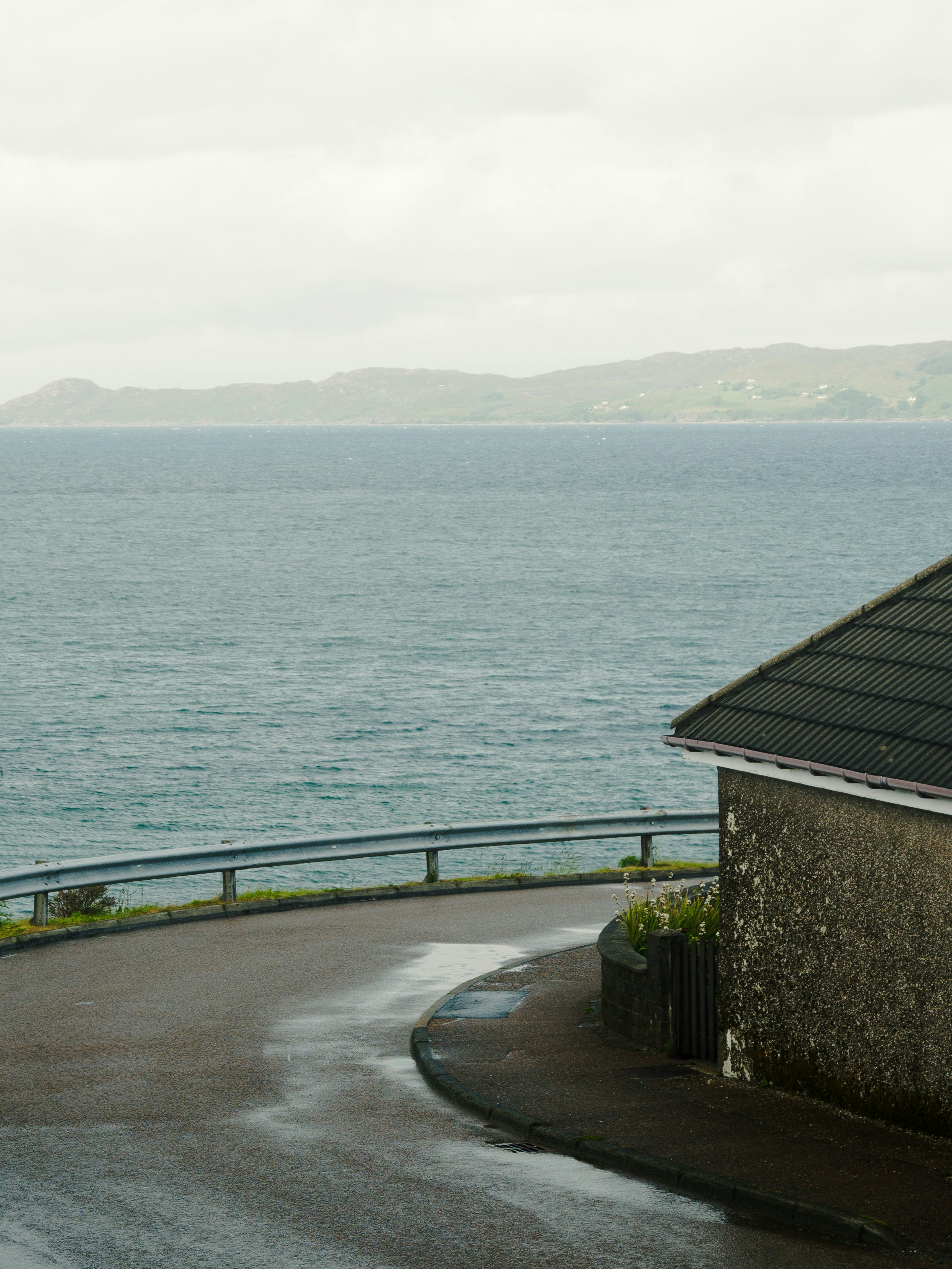 Coastal Curve: Weathered Roof, Quiet Road, and Sea Horizon