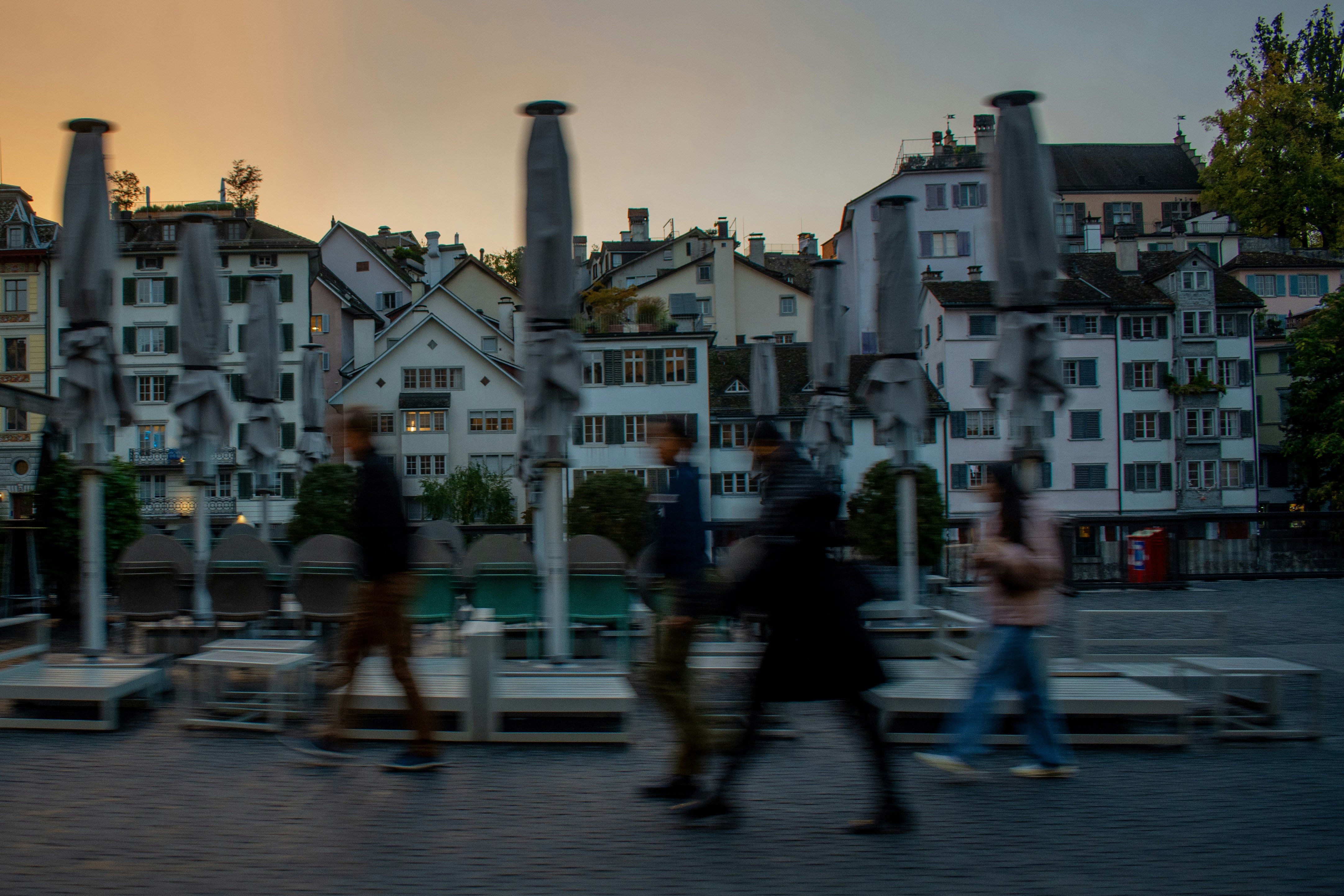 Passants flous à Zurich en fin de journée | People stroll past buildings as the sun sets.
