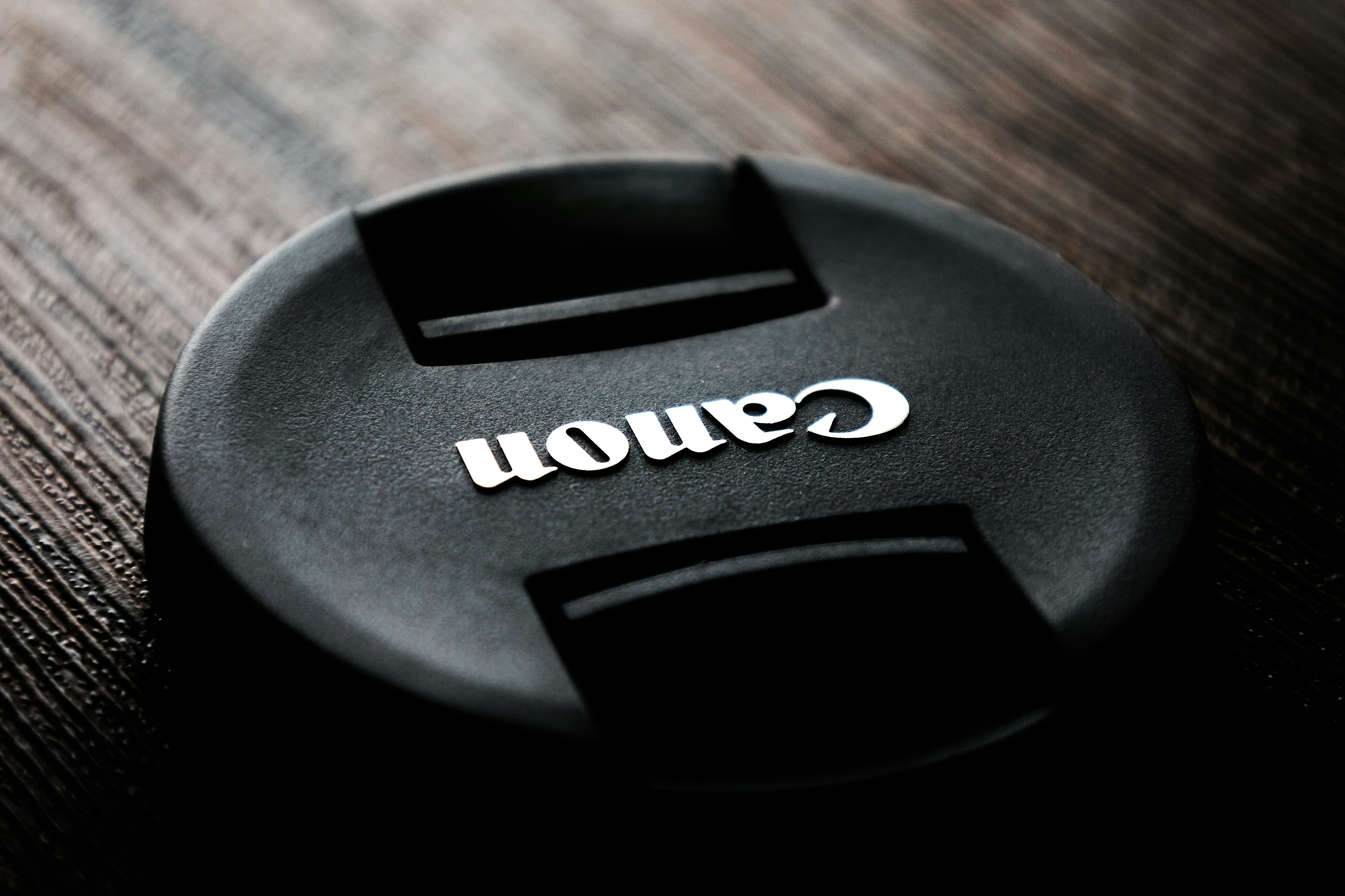 Canon lens cap resting on a textured wooden surface, showcasing its sleek design and branding.