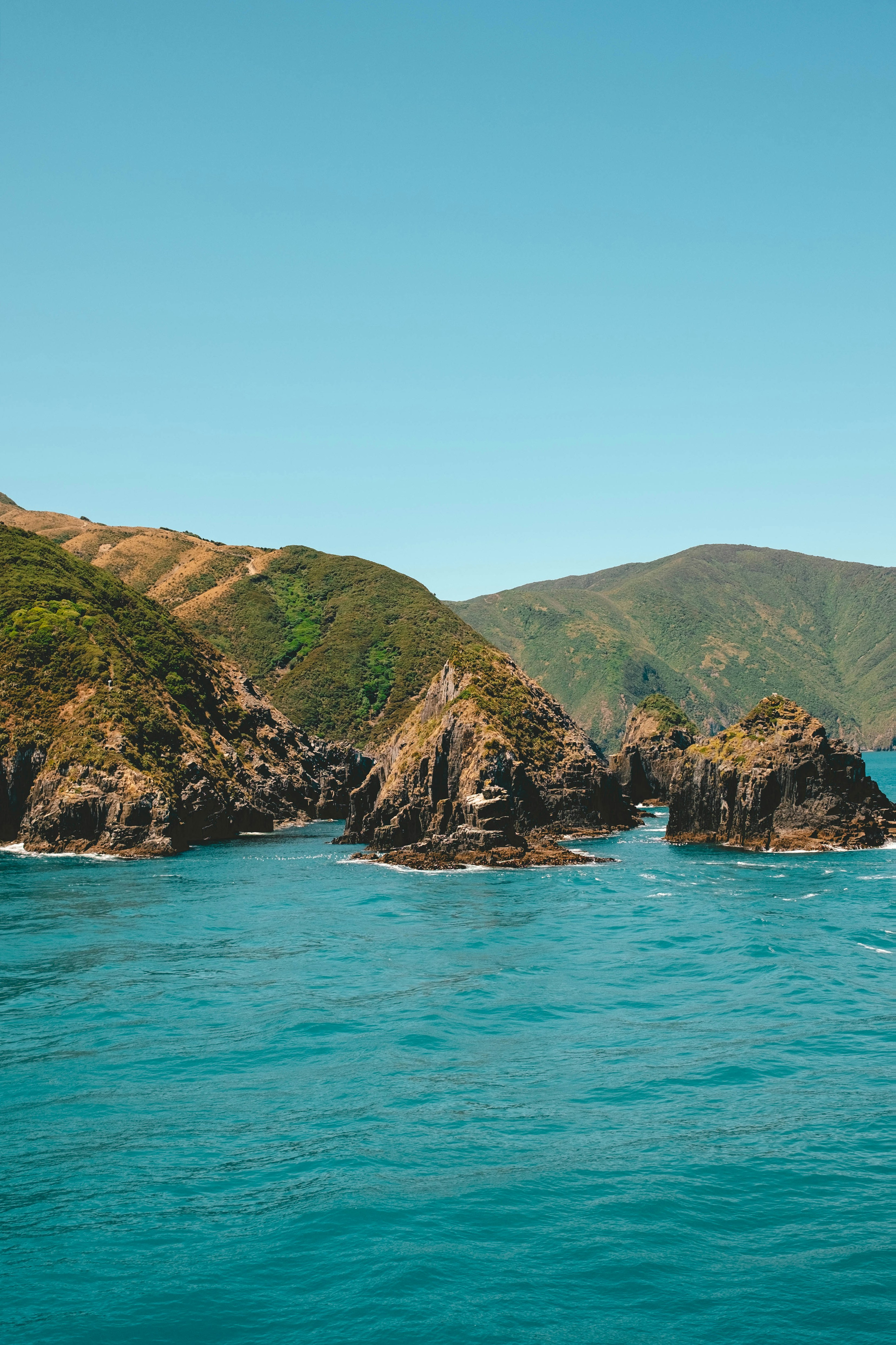Rugged cliffs rise from turquoise waters under a clear blue sky, showcasing the natural beauty of the coastline.