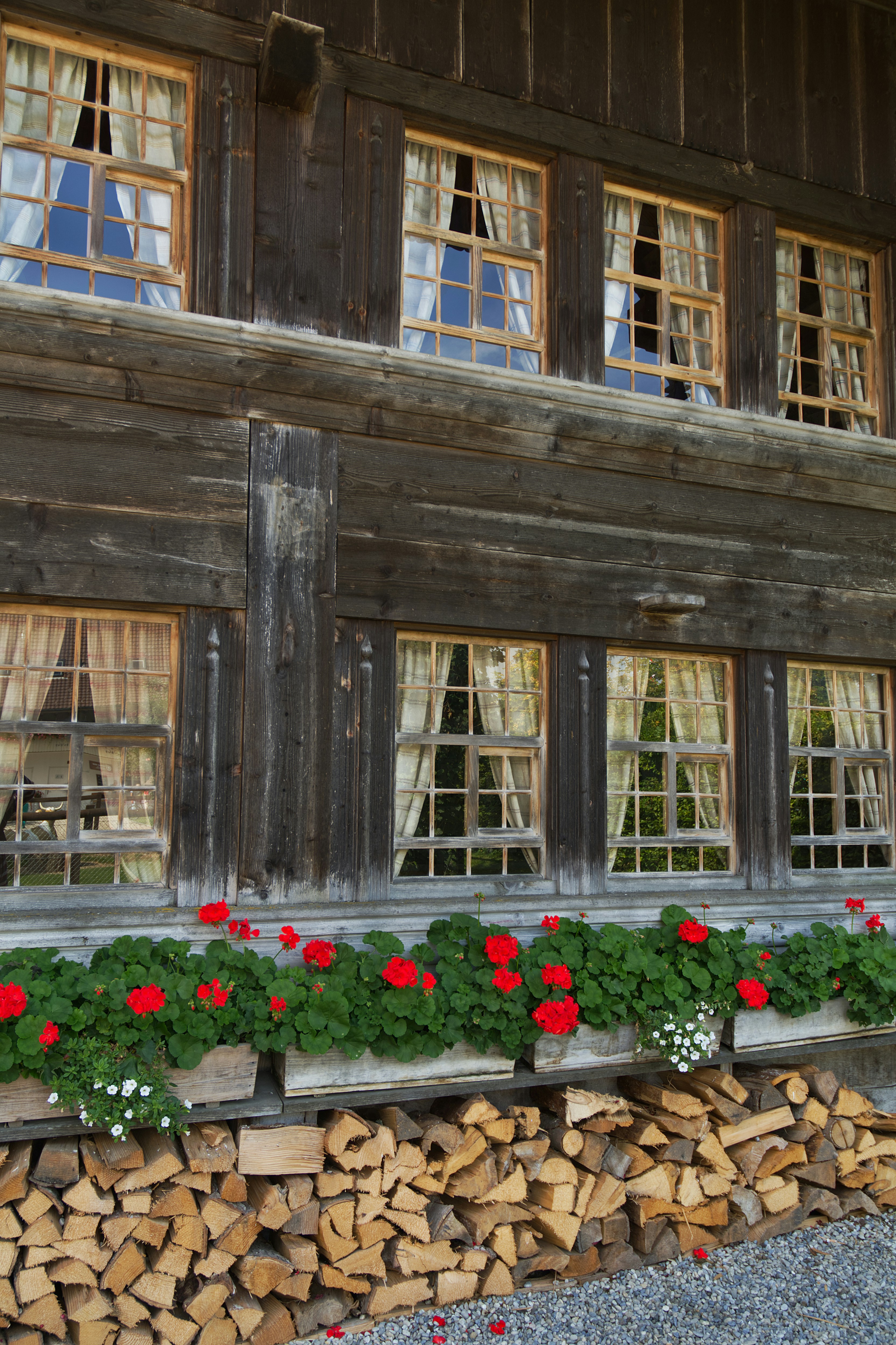 Wooden farmhose wall | Wooden house with windows, flowers, and firewood.