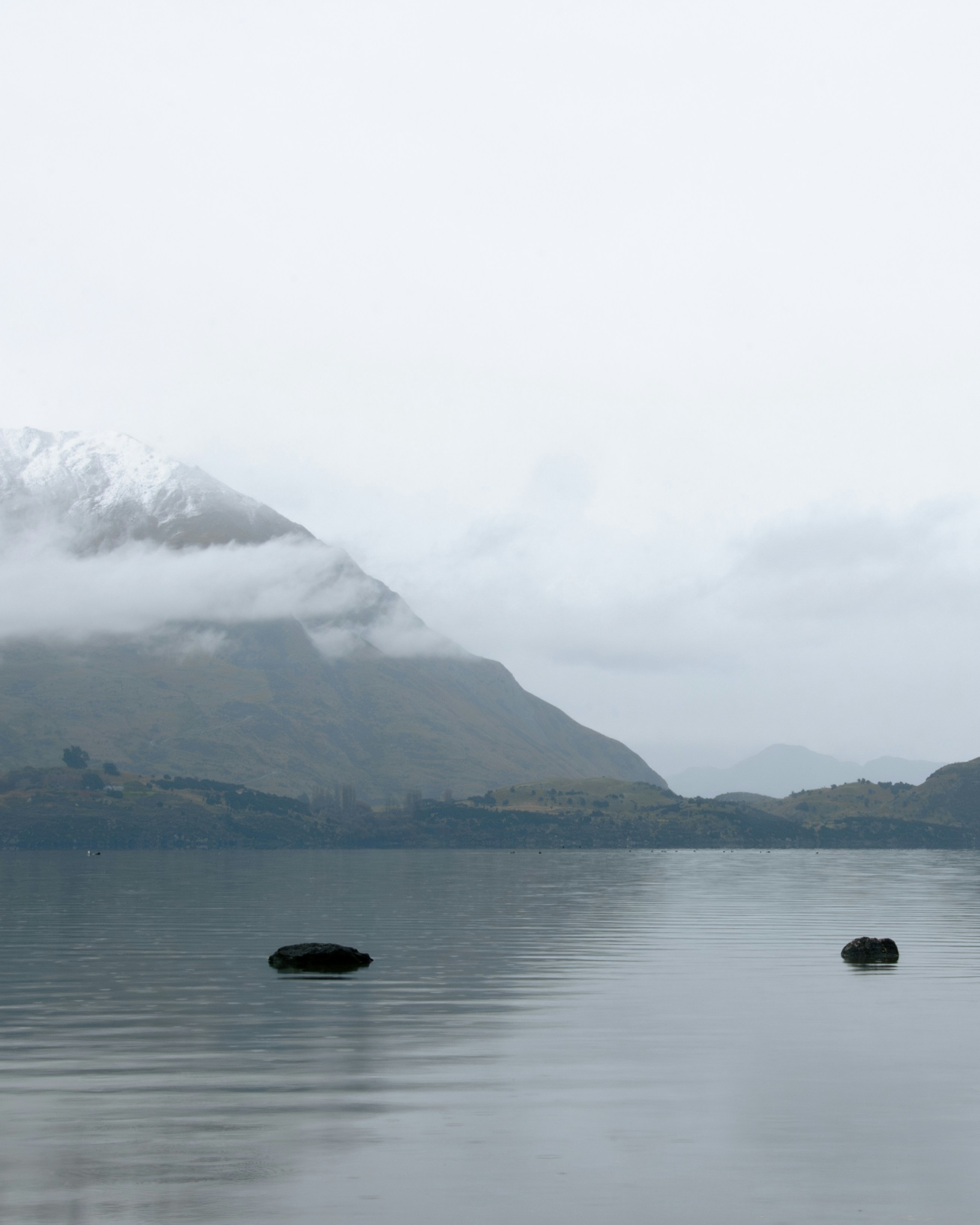 A misty lake and mountains under a cloudy sky.