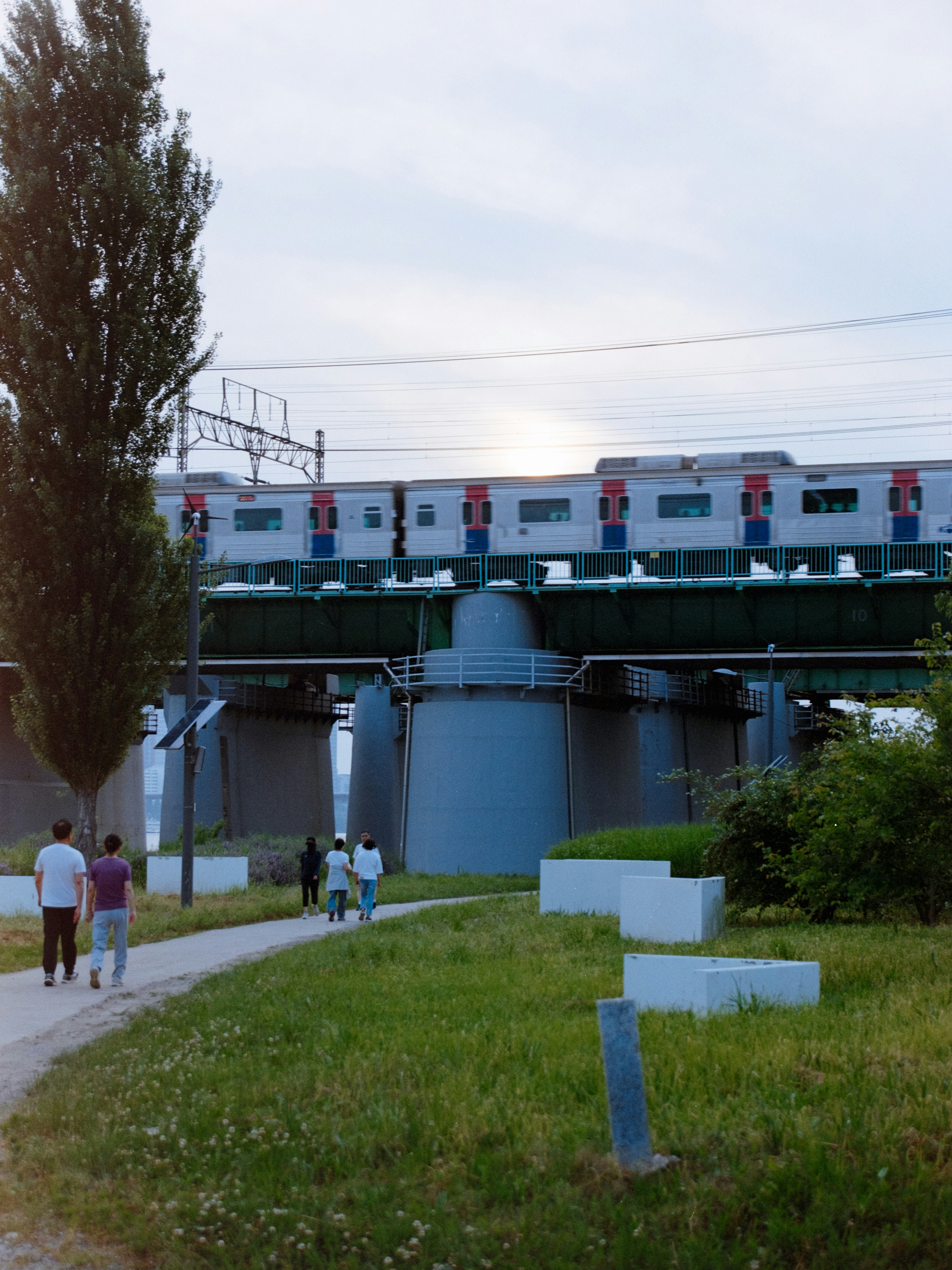 People stroll on a path while a train passes.