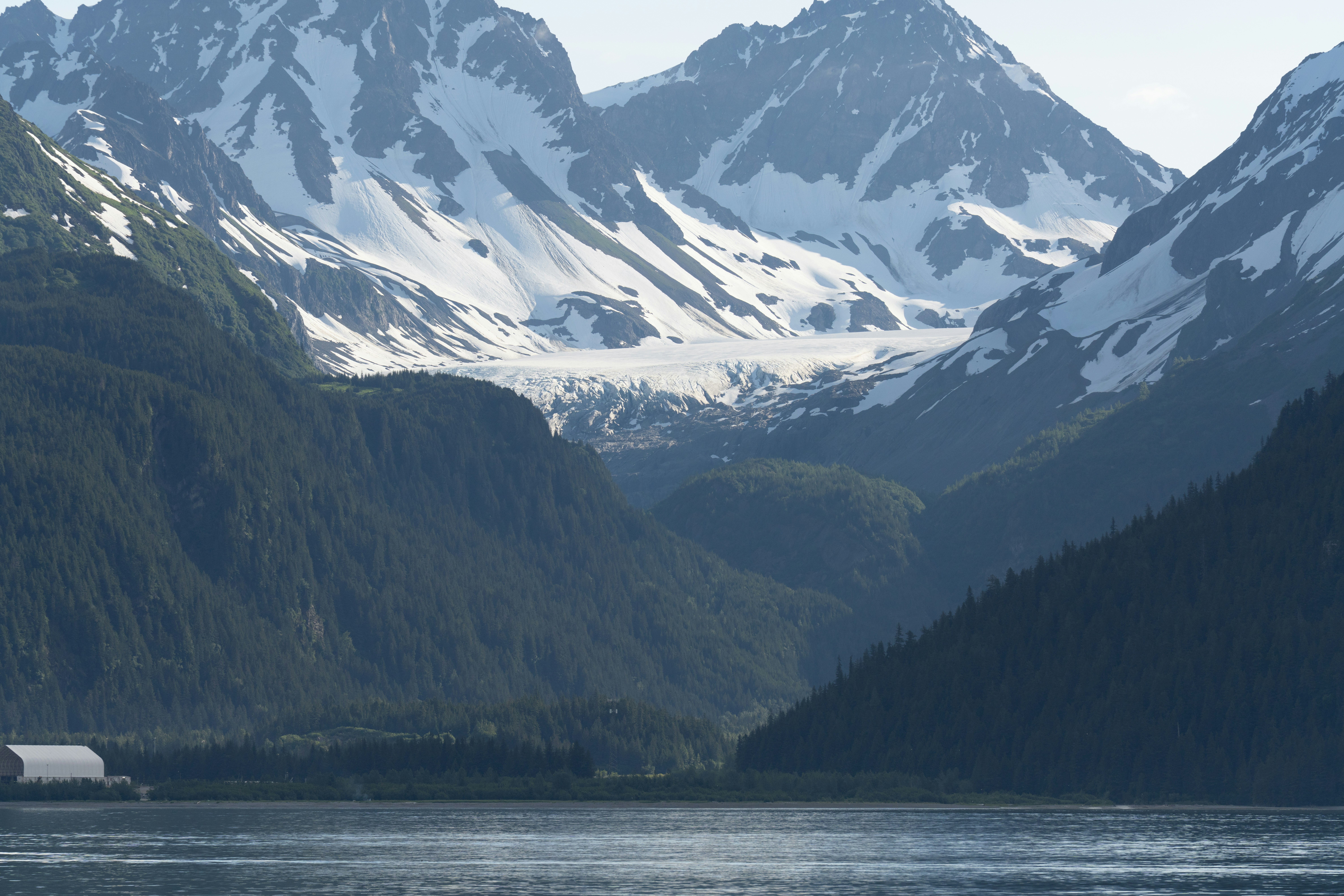Snow-capped mountains rise above a tranquil glacial lake, showcasing the breathtaking beauty of Alaska's natural landscape.
