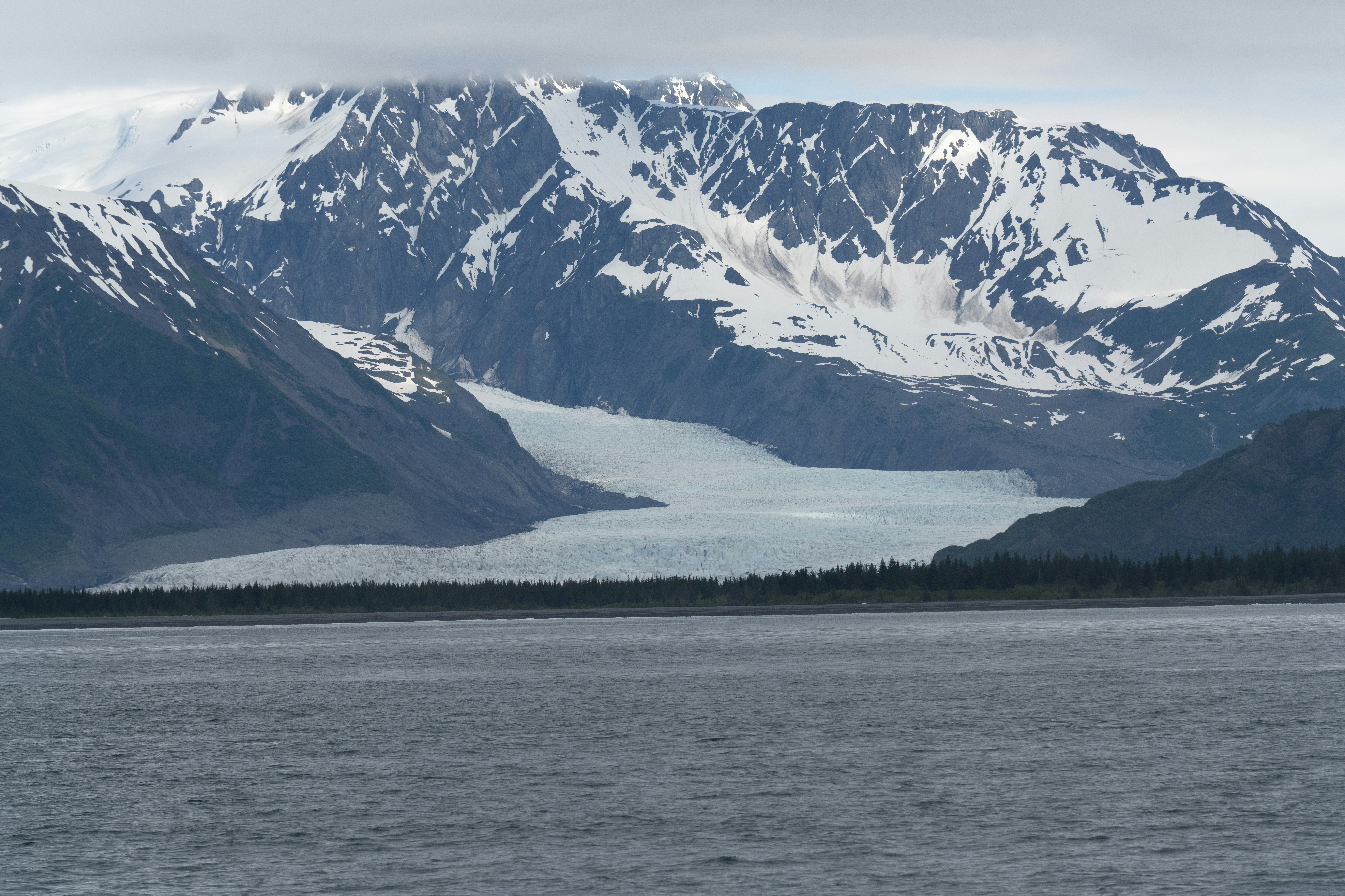 Expansive glacier flowing down from rugged mountains into a serene body of water, showcasing nature's icy artistry.