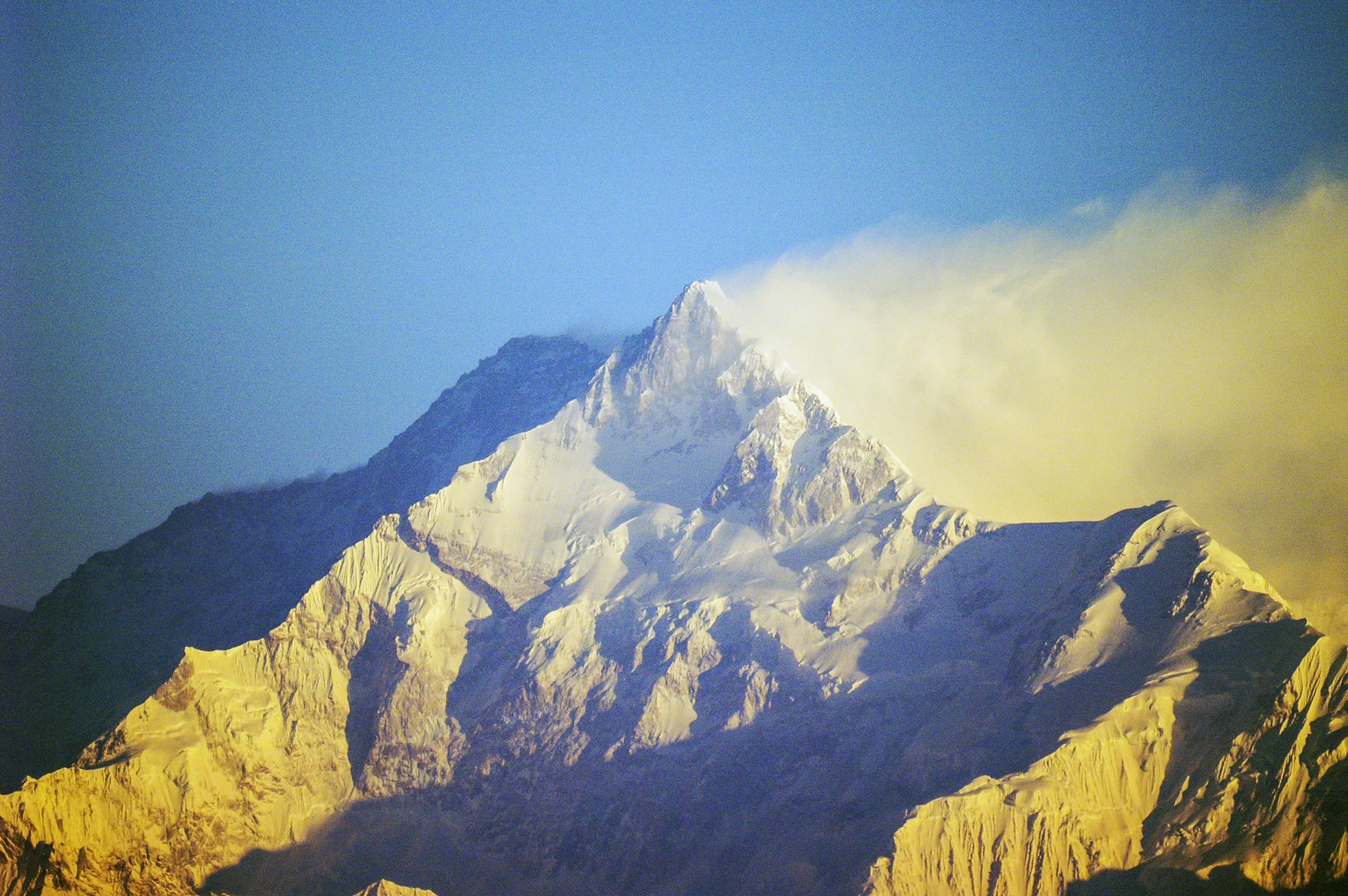 Snow-capped peak bathed in golden light, with wisps of cloud swirling around the summit.