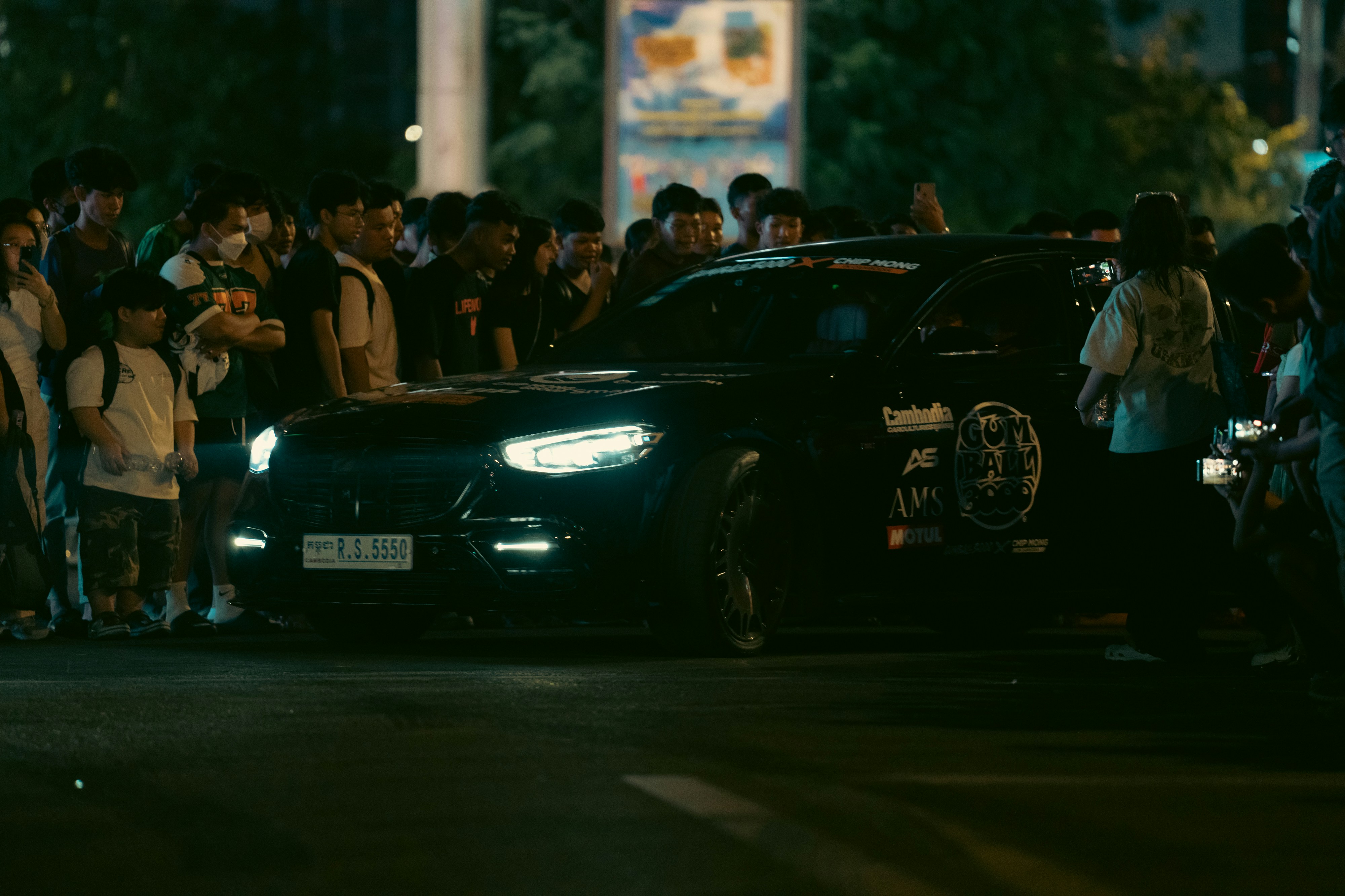 A crowd surrounds a car on a dimly lit street. photo – Free Car Image ...