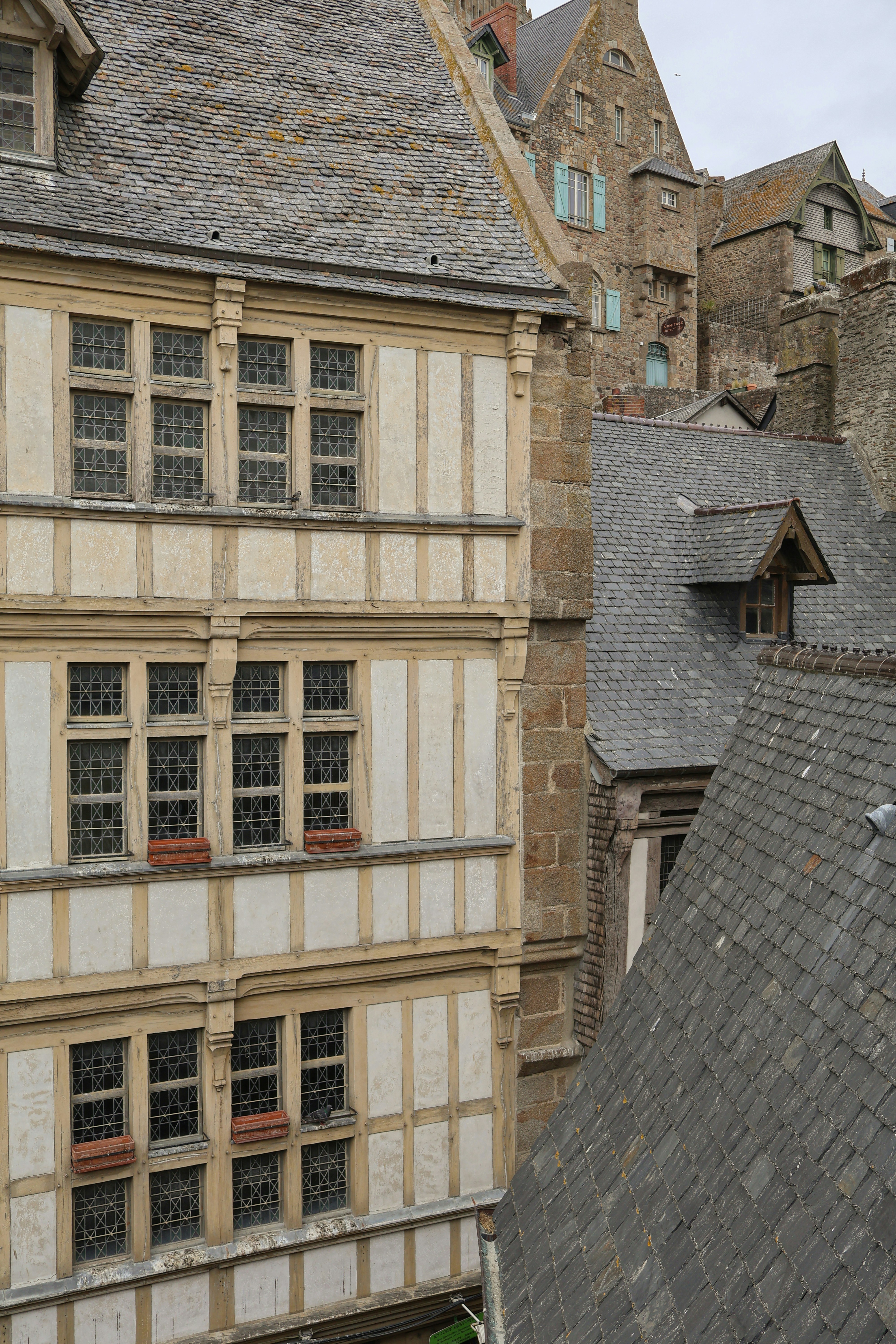 Stacked old houses in Mont Saint Michel, France | Old buildings with detailed architecture are visible.