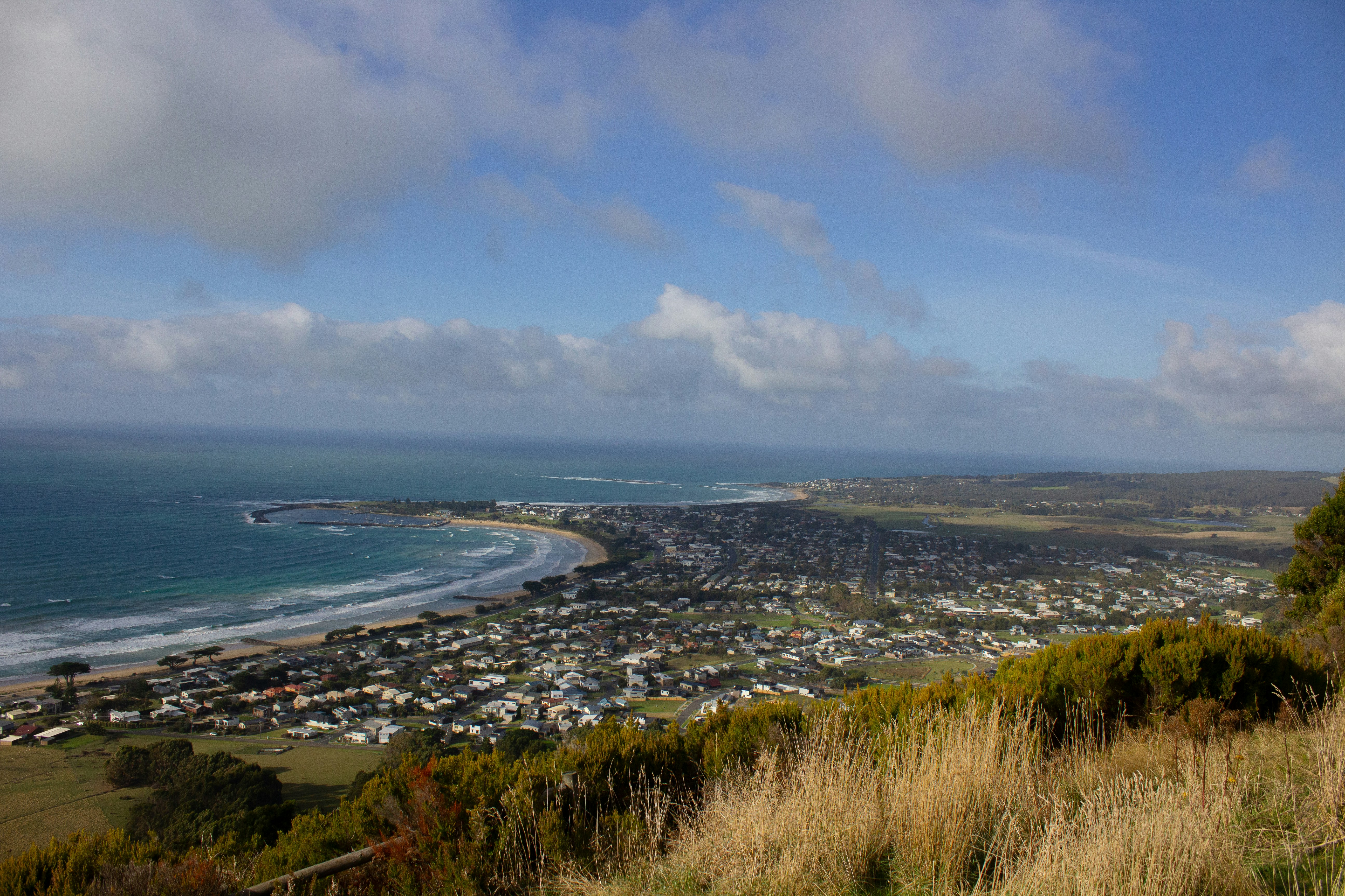 Panoramic view of a coastal town with lush greenery and rolling waves, showcasing the blend of urban and natural landscapes.