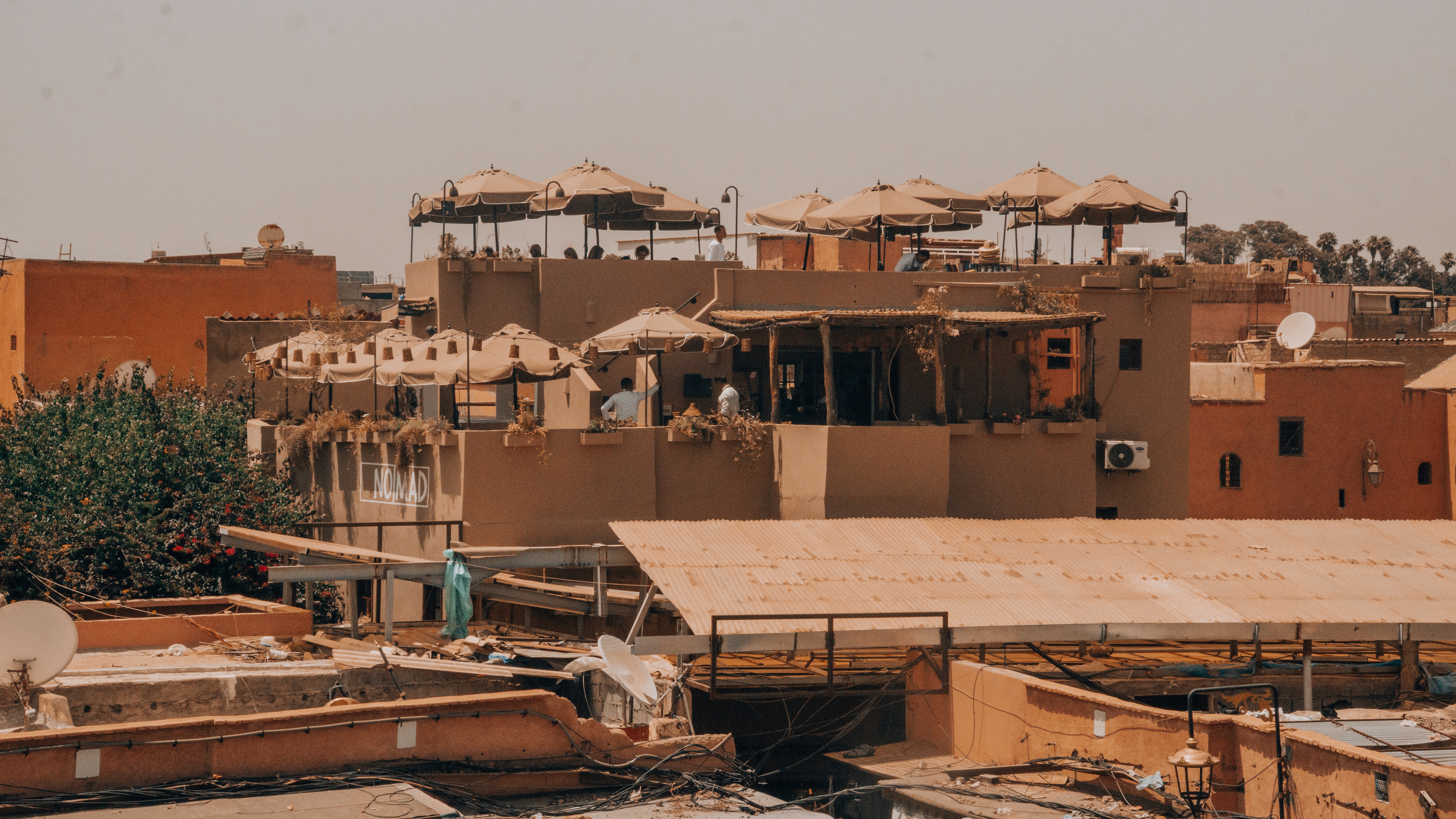 Rooftops adorned with sunshades and greenery in a bustling urban setting, showcasing the architectural charm of the area. A blend of modern and traditional elements creates a unique skyline.