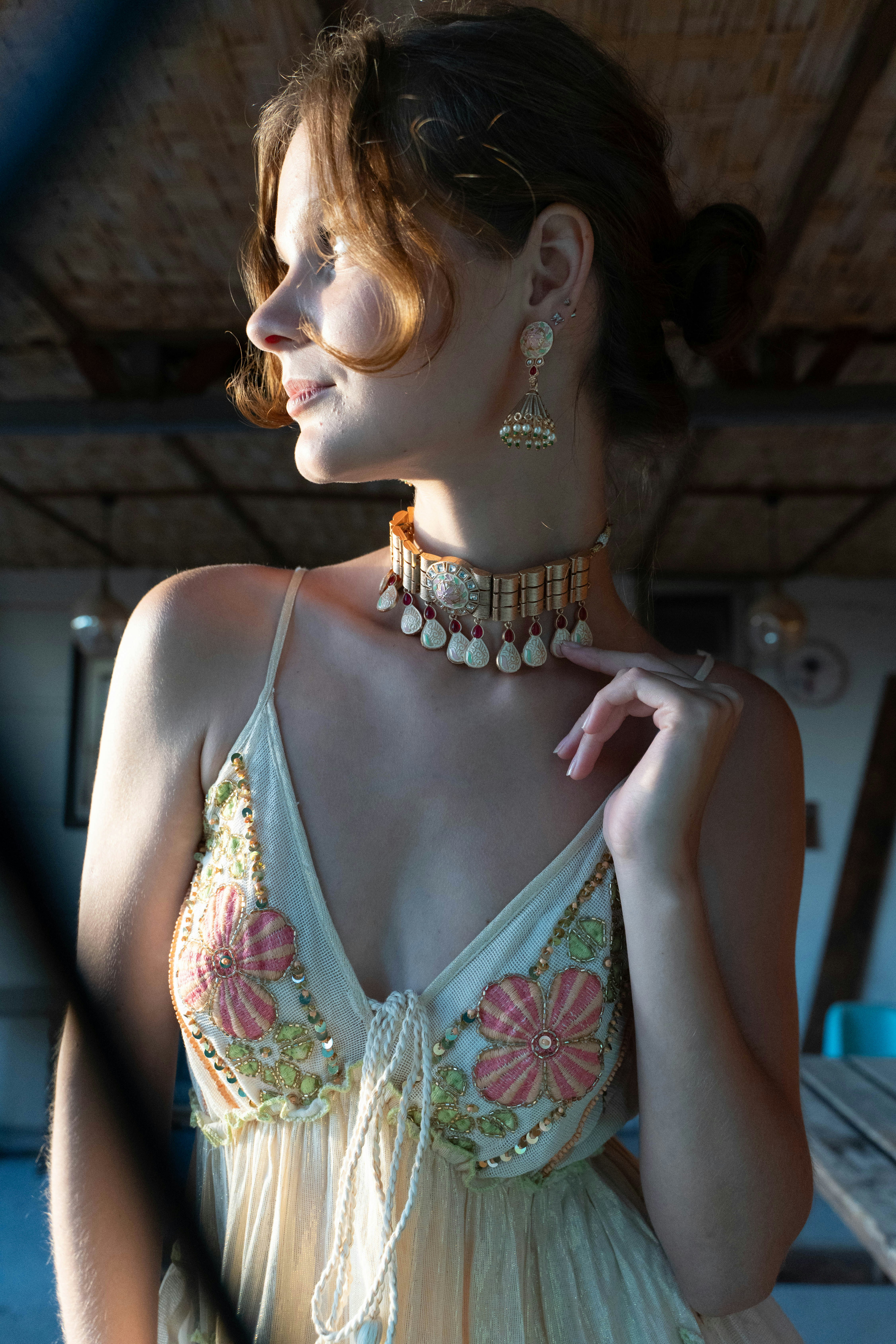 A woman adorned in a delicately embroidered dress and statement jewelry, captured in golden hour light, exuding grace and charm.