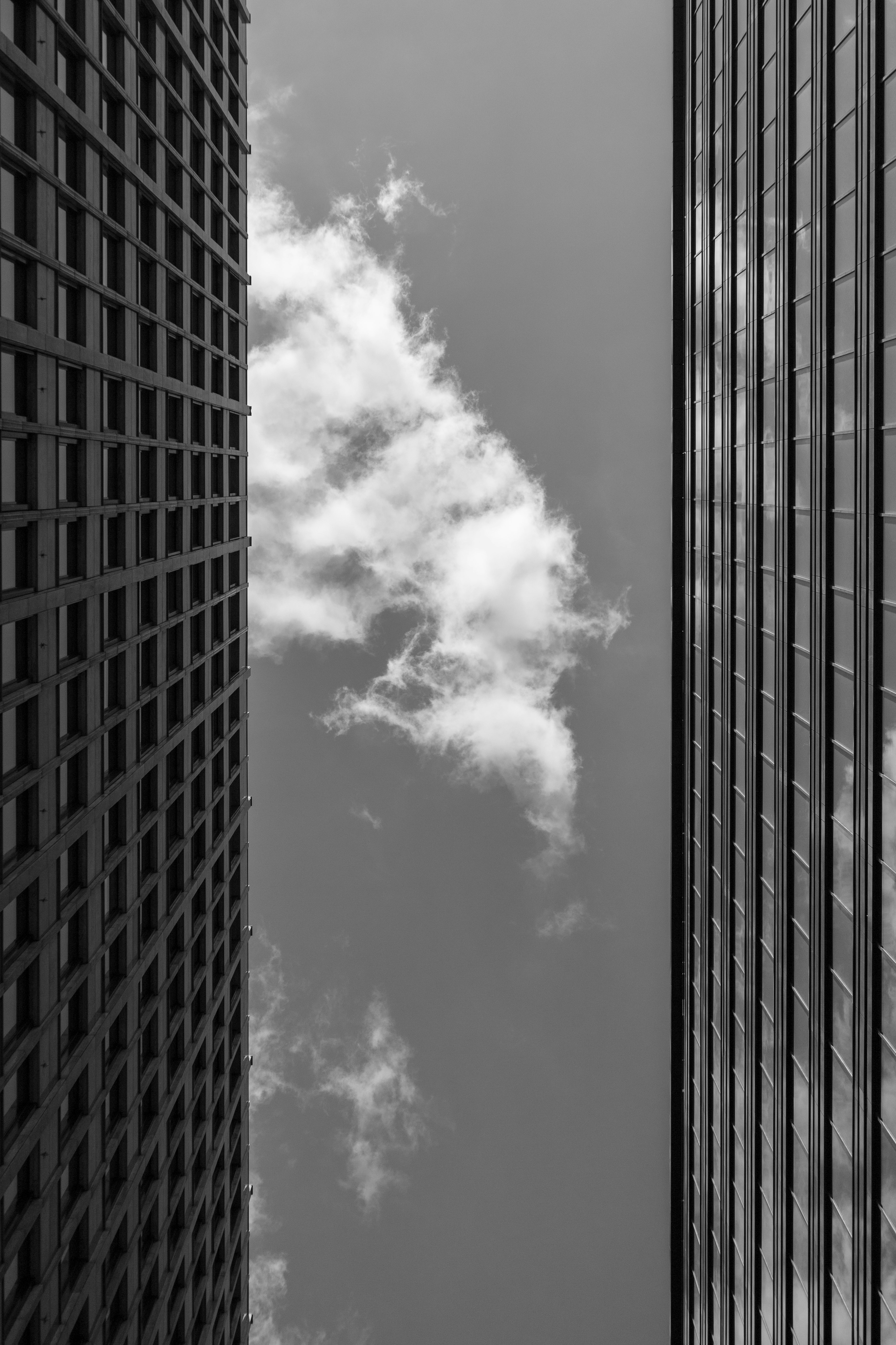 Monochrome view of a cloudy sky framed by towering buildings, emphasizing the contrast between architecture and nature.