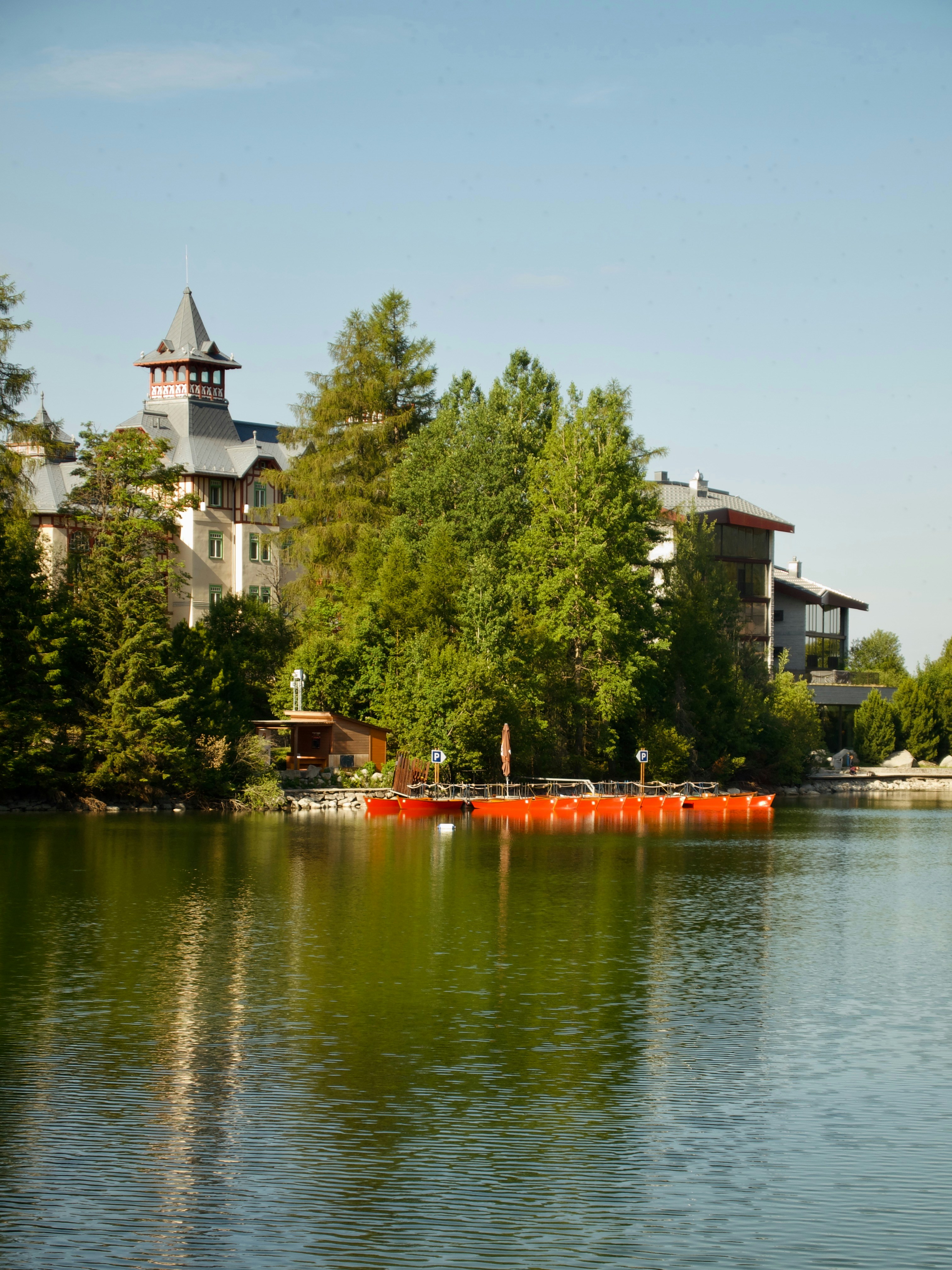 Red boats | Lake view with buildings and trees.