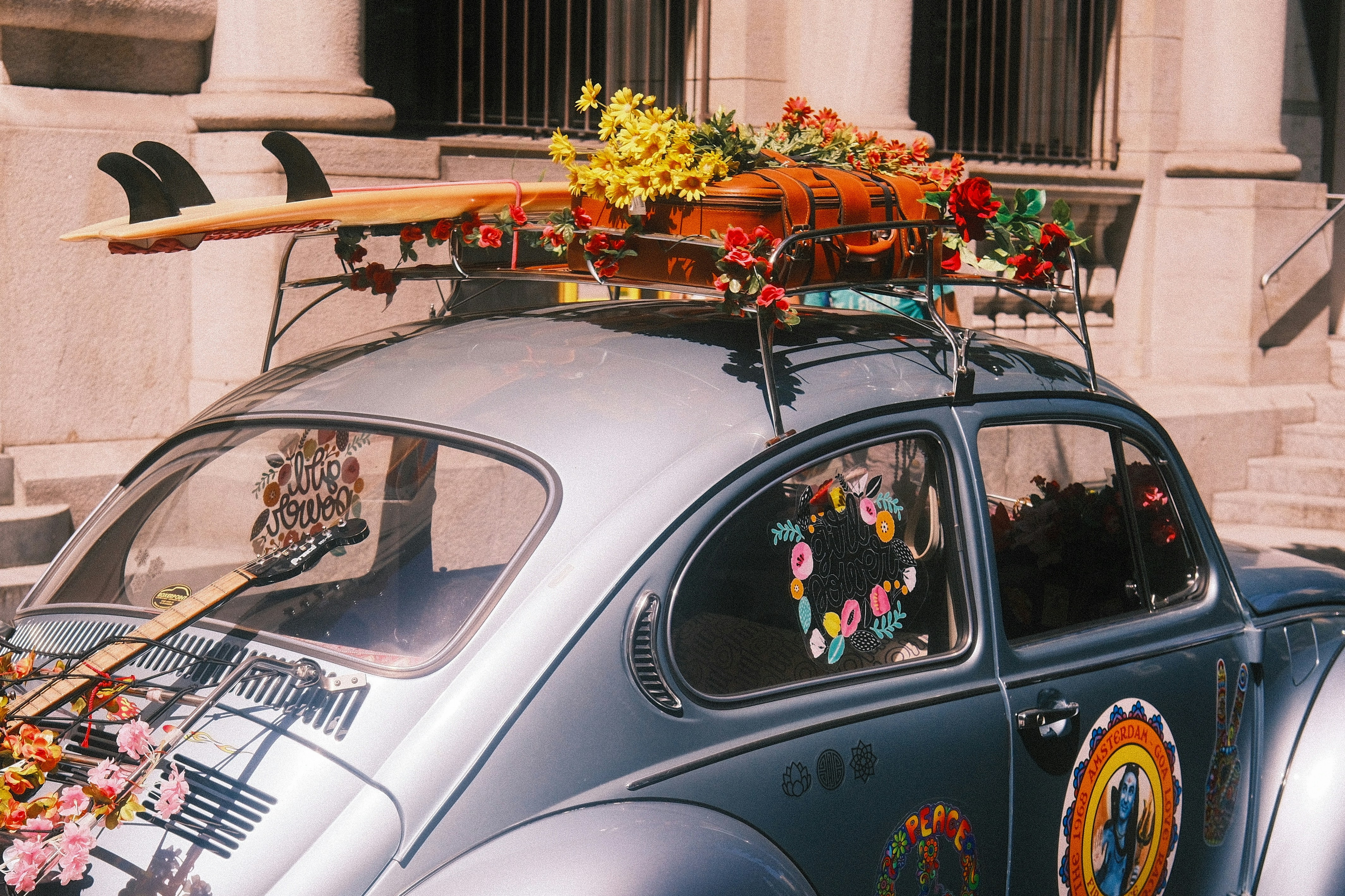 peacemaker. | A volkswagen beetle is decorated with flowers and a surfboard.