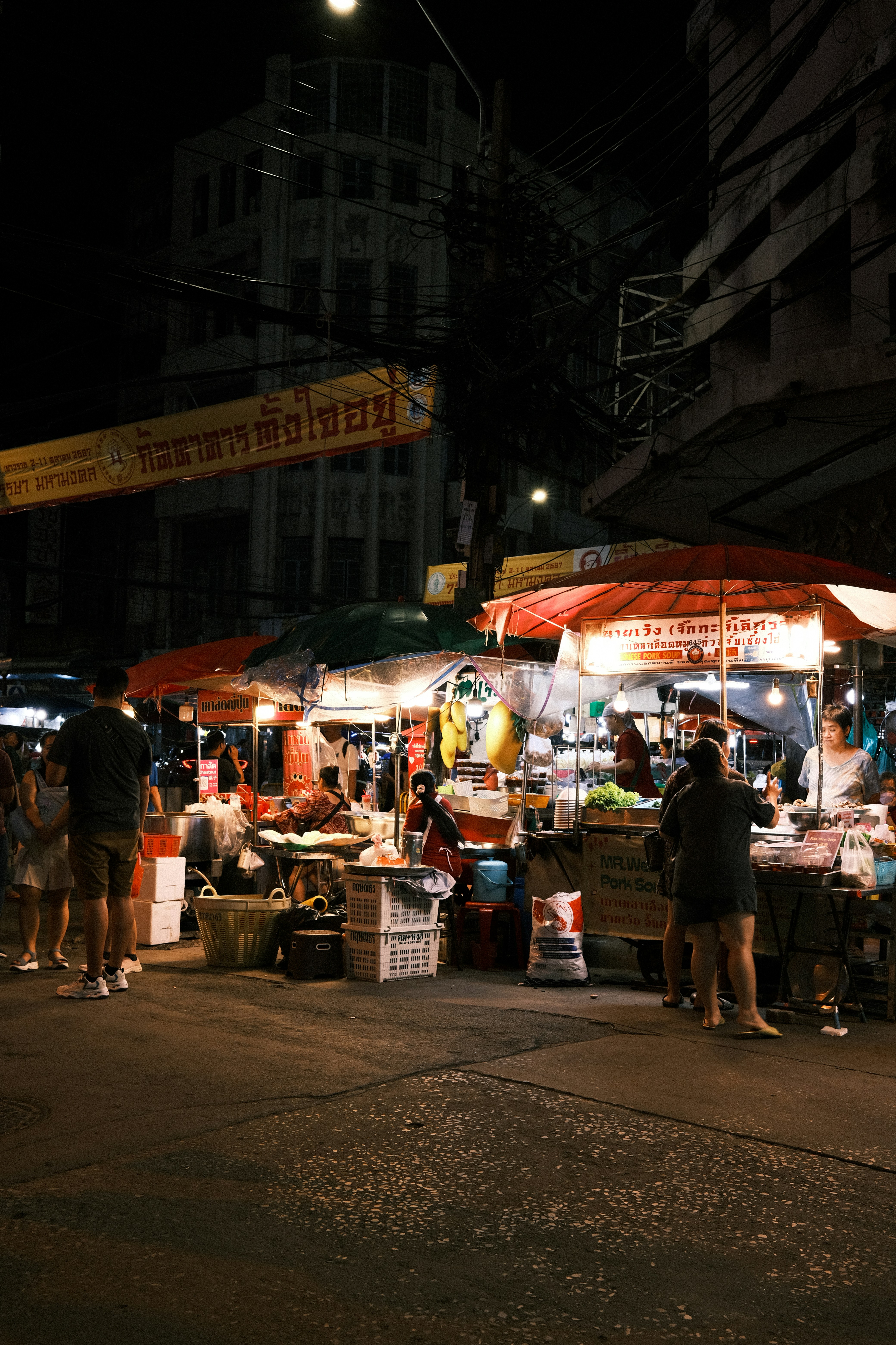 Vibrant street market bustling with vendors and shoppers under colorful umbrellas at night.