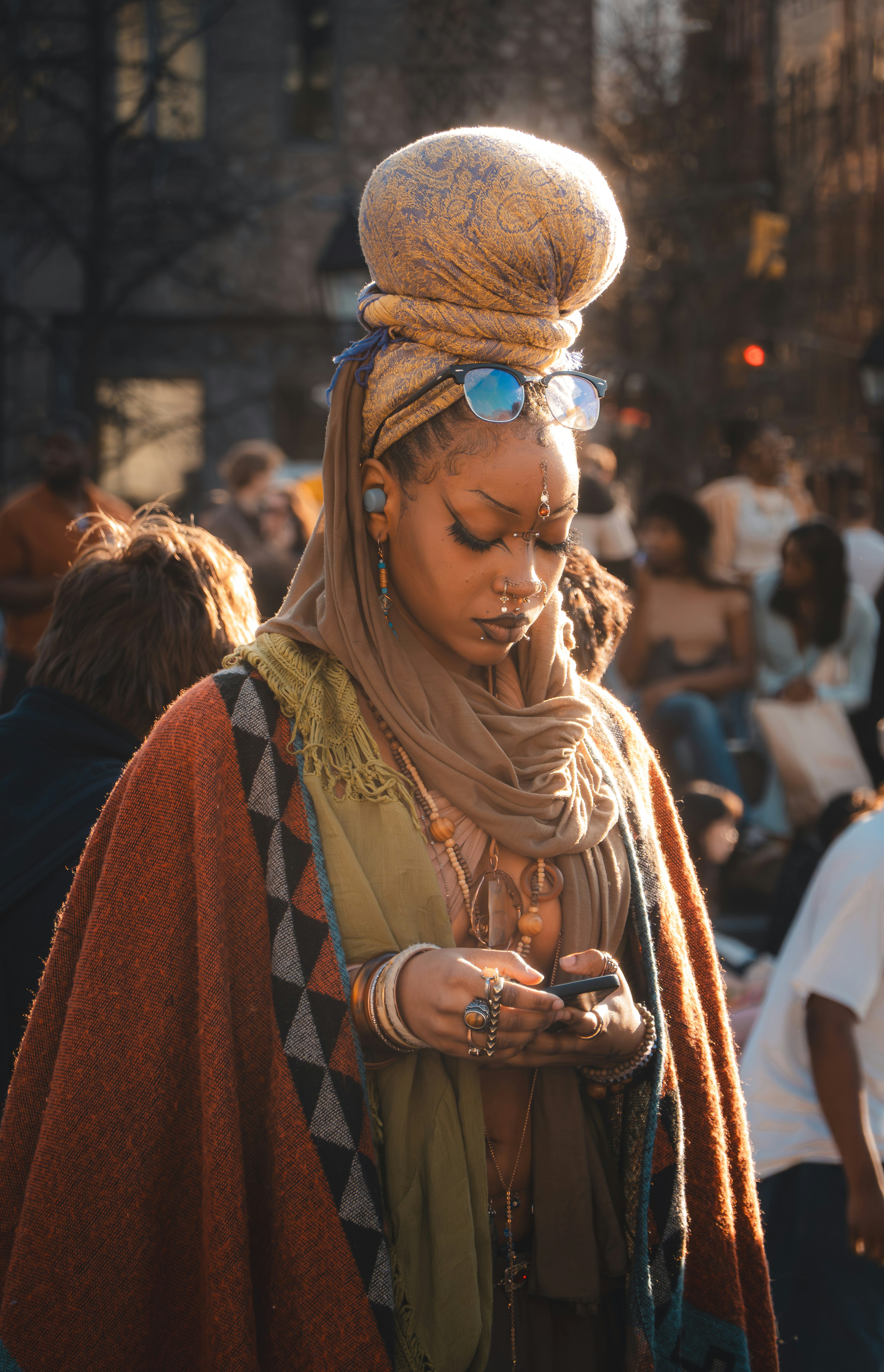 A woman adorned in vibrant textiles and intricate jewelry gazes at her phone, embodying a blend of tradition and modernity. The warm sunlight enhances the rich colors of her attire.