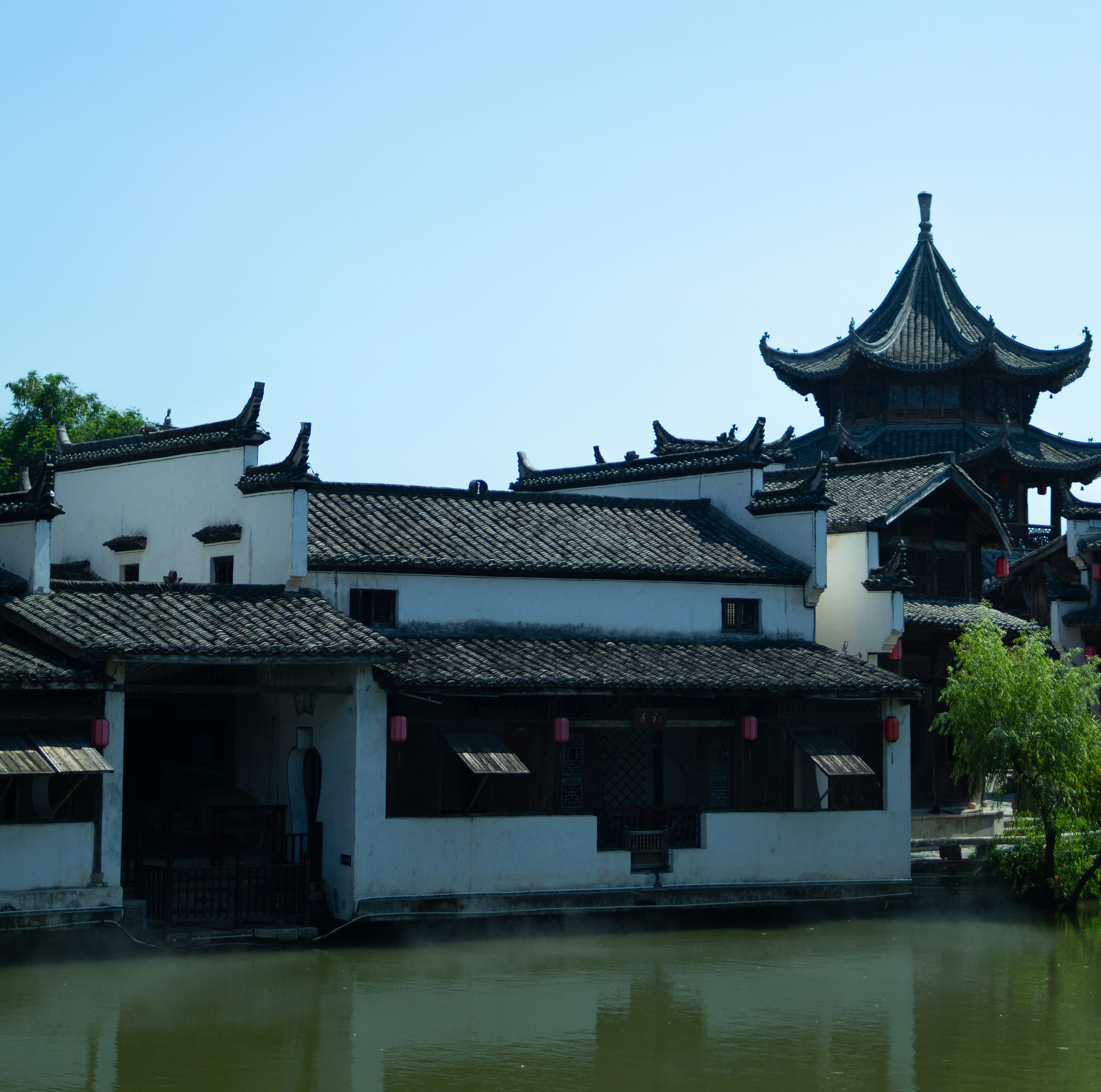 Chinese architecture stands beside tranquil water.
