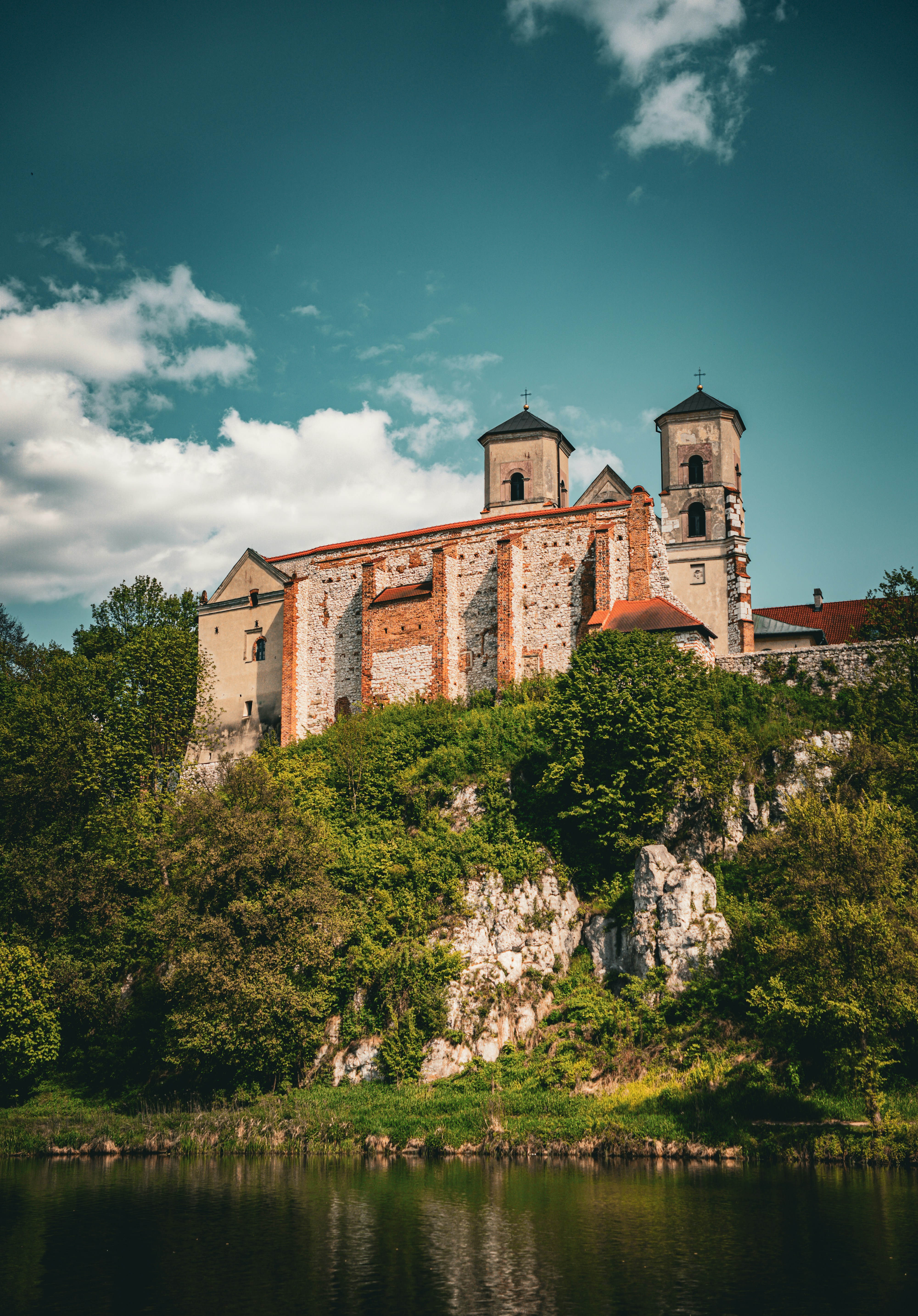 Ancient stone ruins perched on a hillside, surrounded by lush greenery and reflecting in the calm river below.