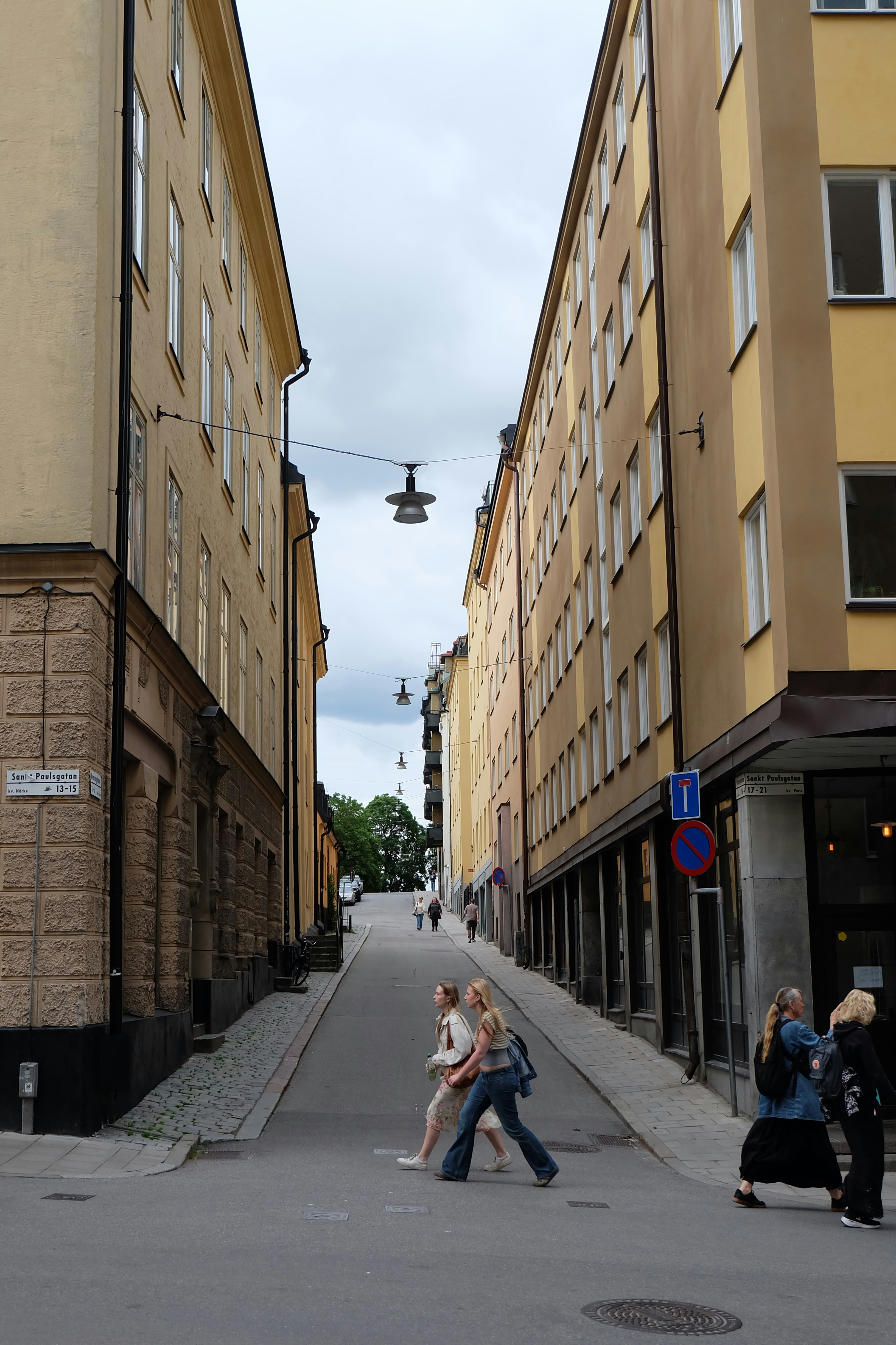 Two pedestrians crossing a cobblestone street flanked by charming buildings in a historical urban setting.