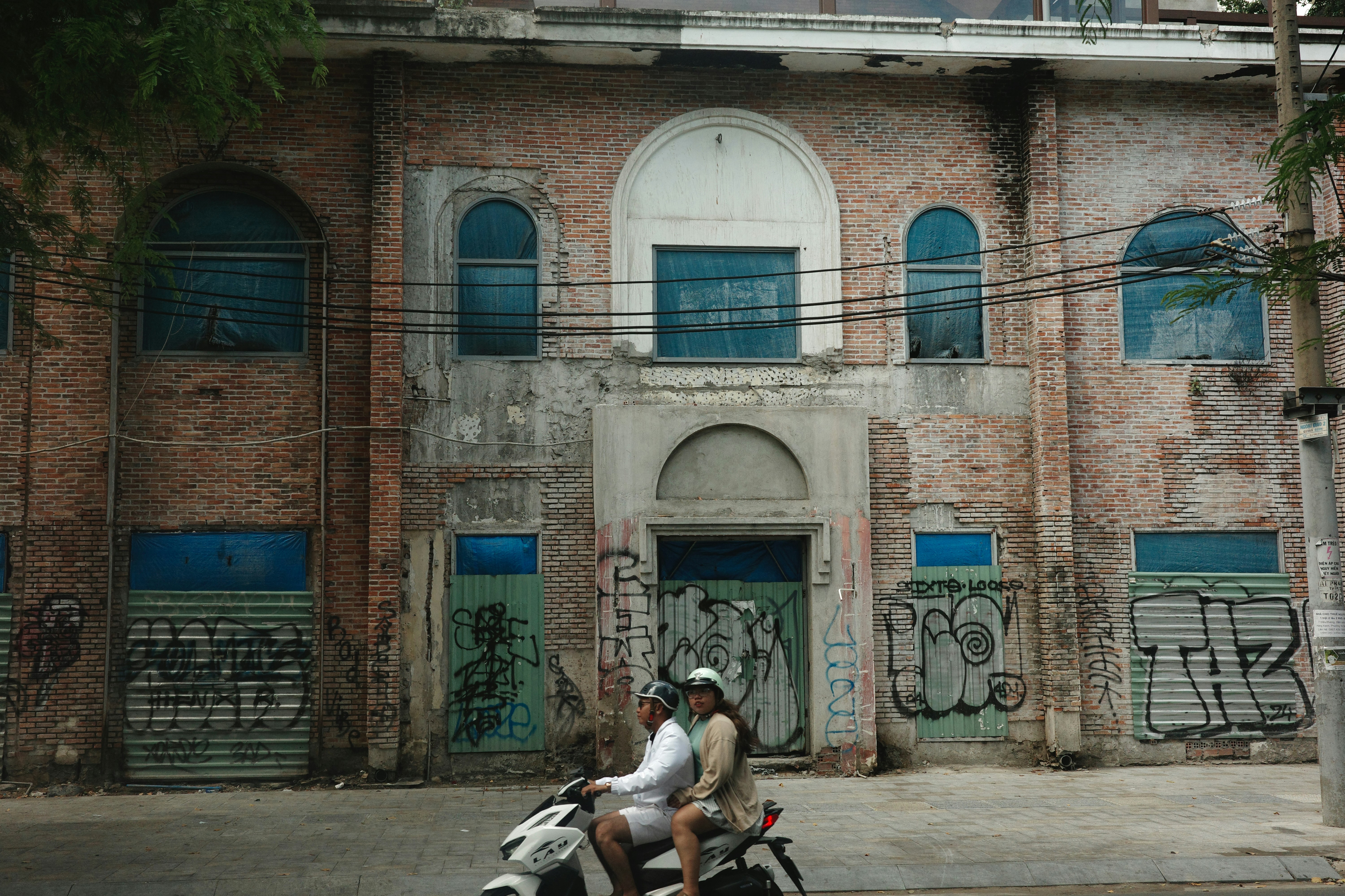 A couple rides a scooter in front of a building.