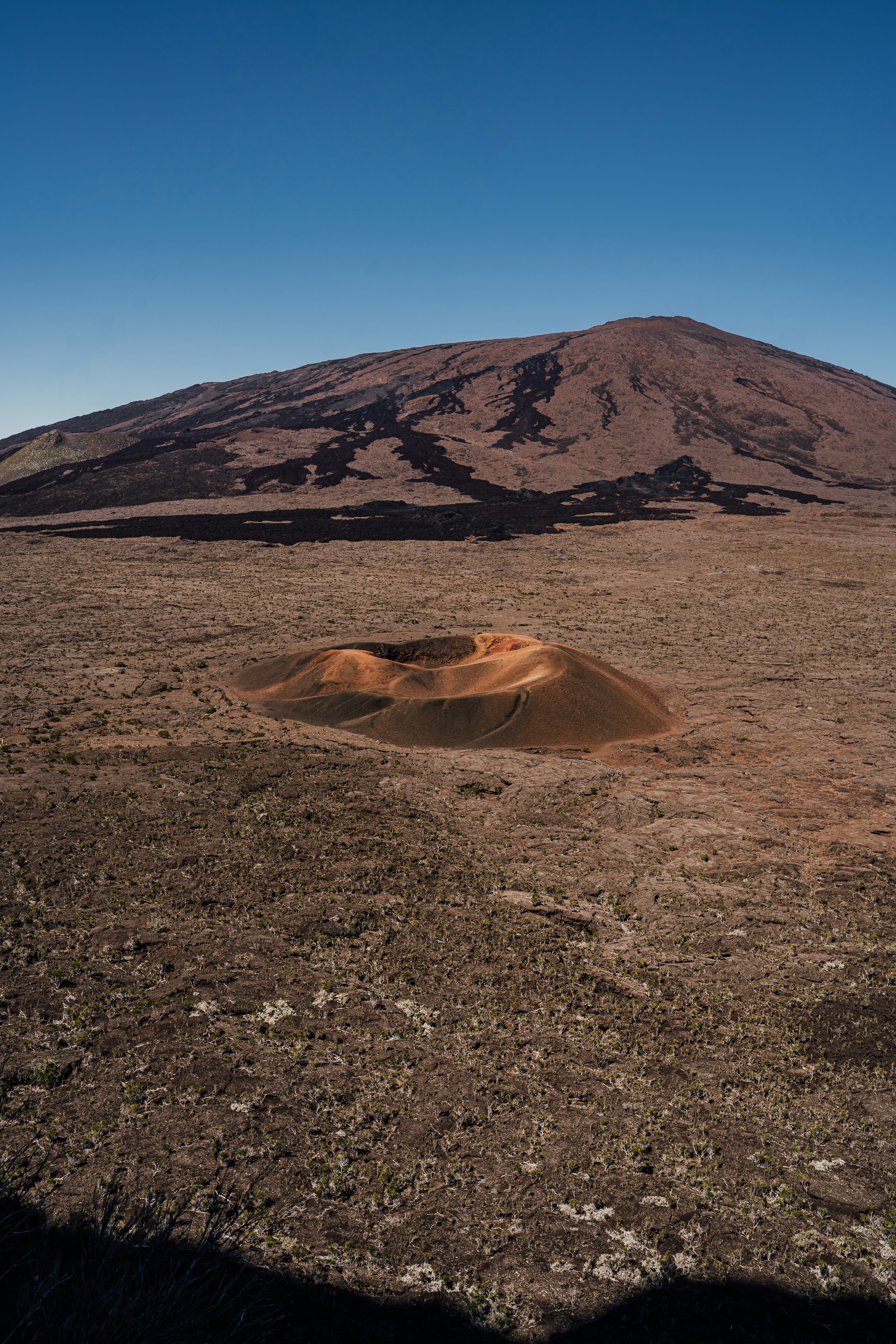 A unique volcanic crater surrounded by arid land, with a prominent mountain in the background showcasing geological formations.
