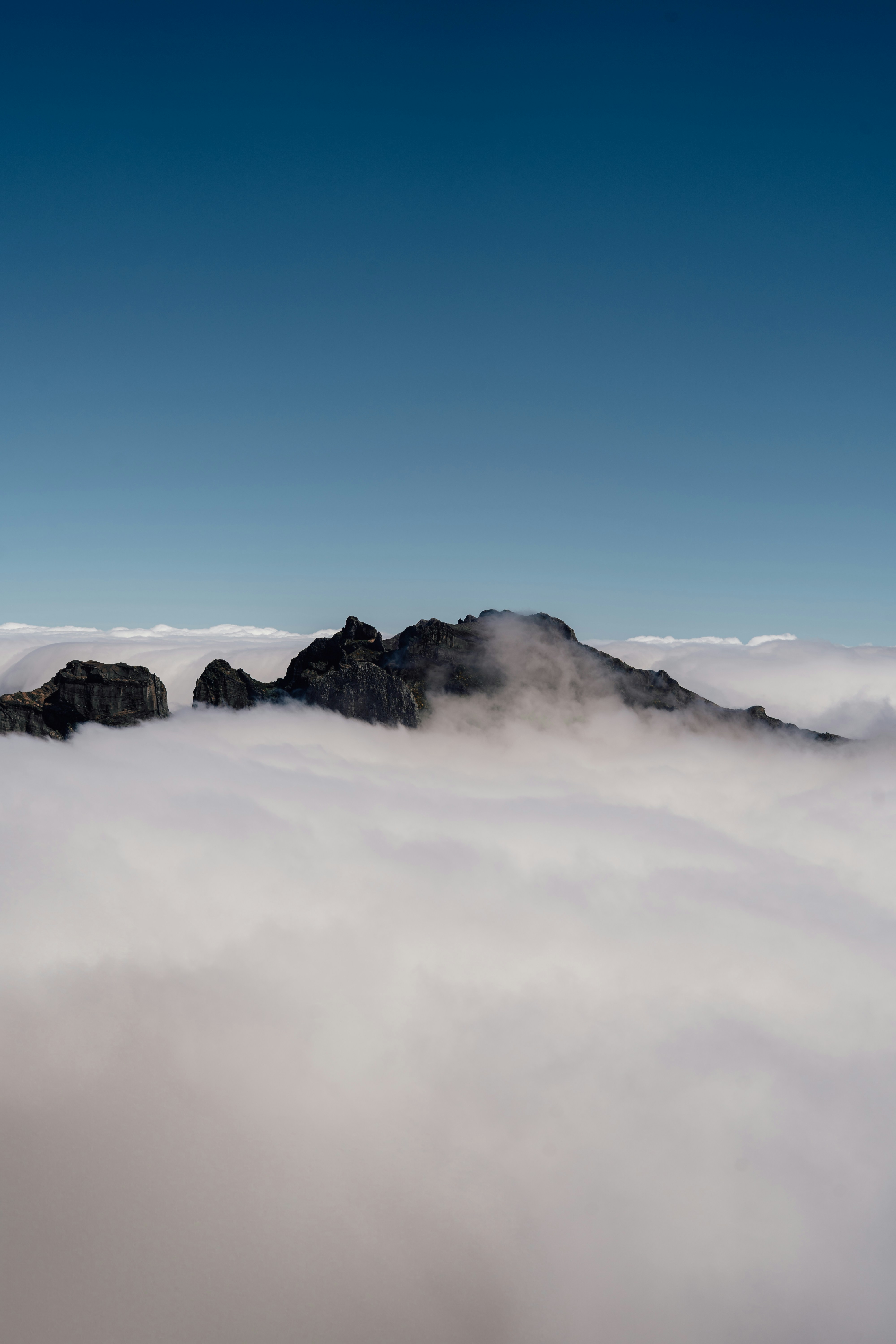 Mountain peaks emerge from a thick blanket of clouds under a clear blue sky.