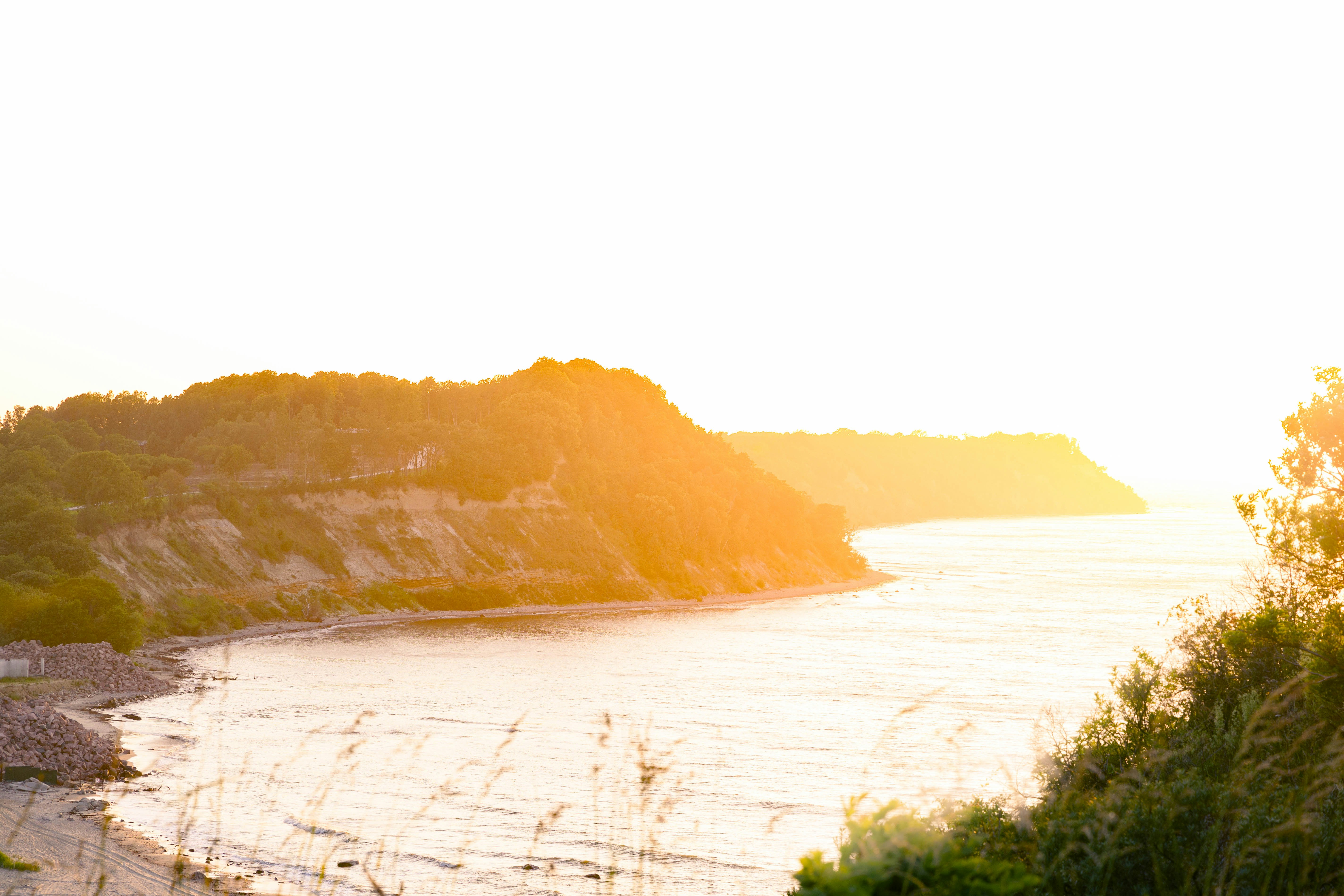 Sunset illuminating the coastline with vibrant hues, where land meets the gentle waves of the sea. Lush greenery frames the serene landscape.