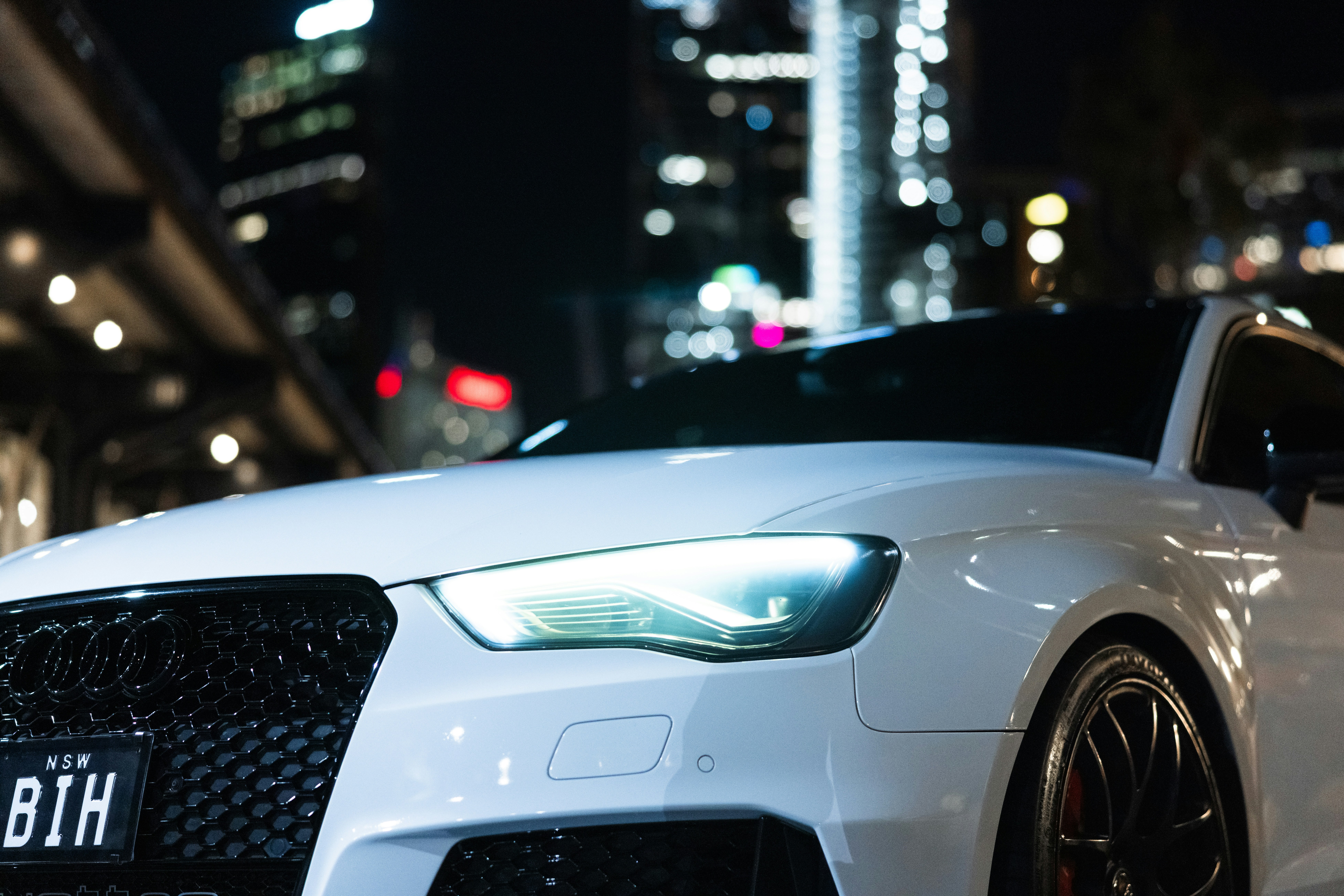 Sleek white Audi RS5 parked under city lights, showcasing its striking design and illuminated headlights.