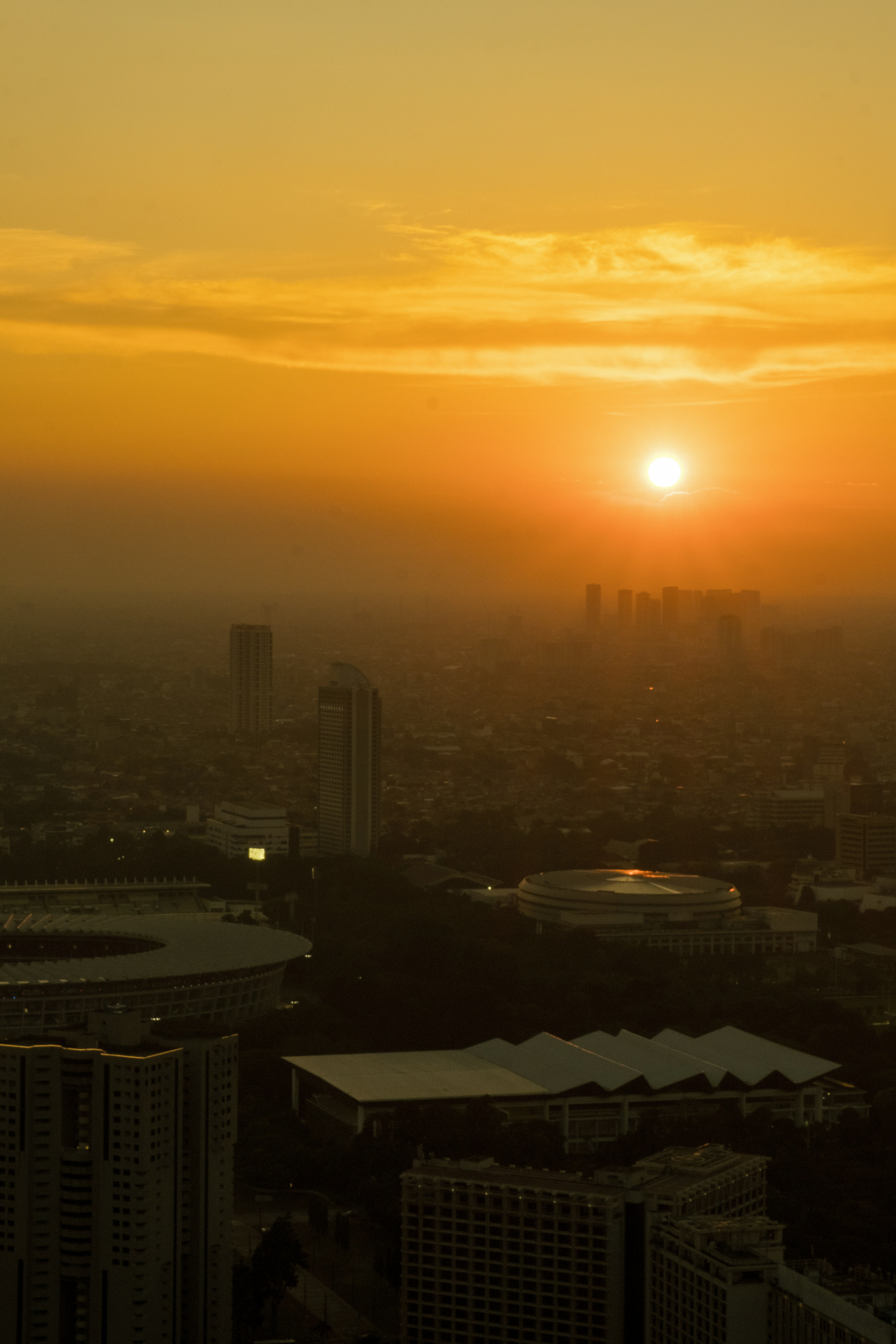Golden sunset illuminating a sprawling cityscape, with silhouettes of skyscrapers and sports venues below.