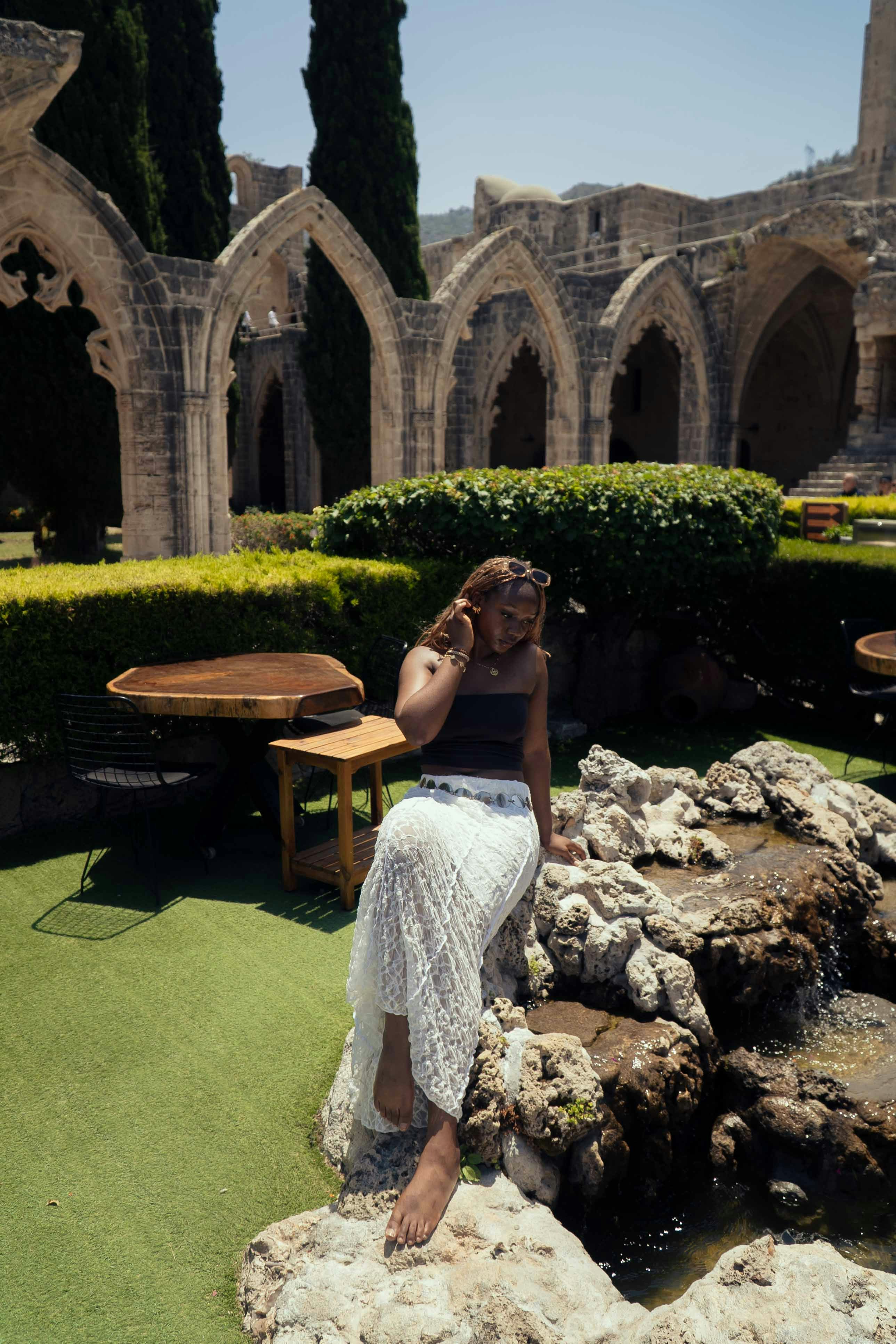 Woman poses by water with an ancient architectural background.
